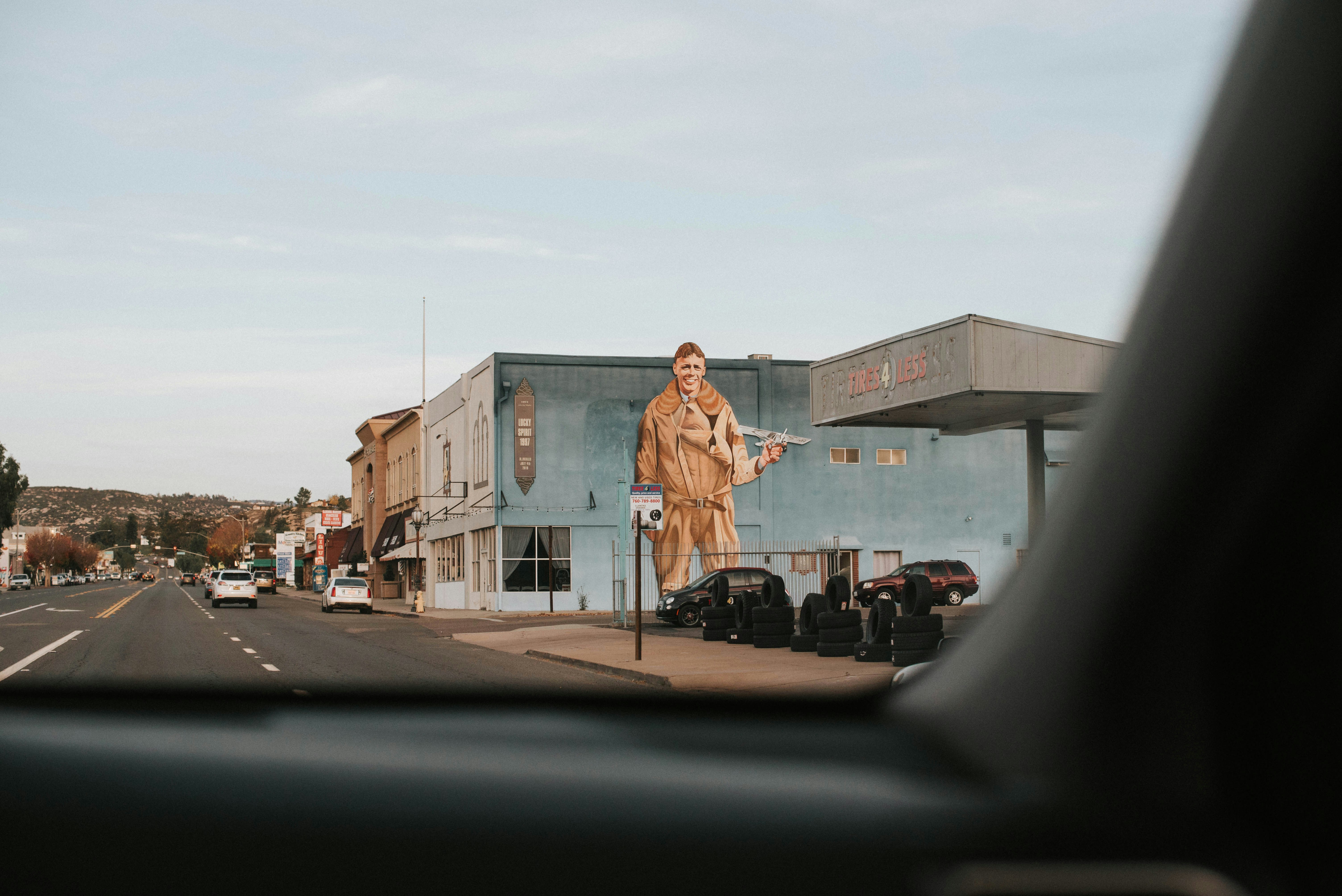 Main Street Giant: A tan-suited statue anchors a pastel-blue storefront along a quiet boulevard