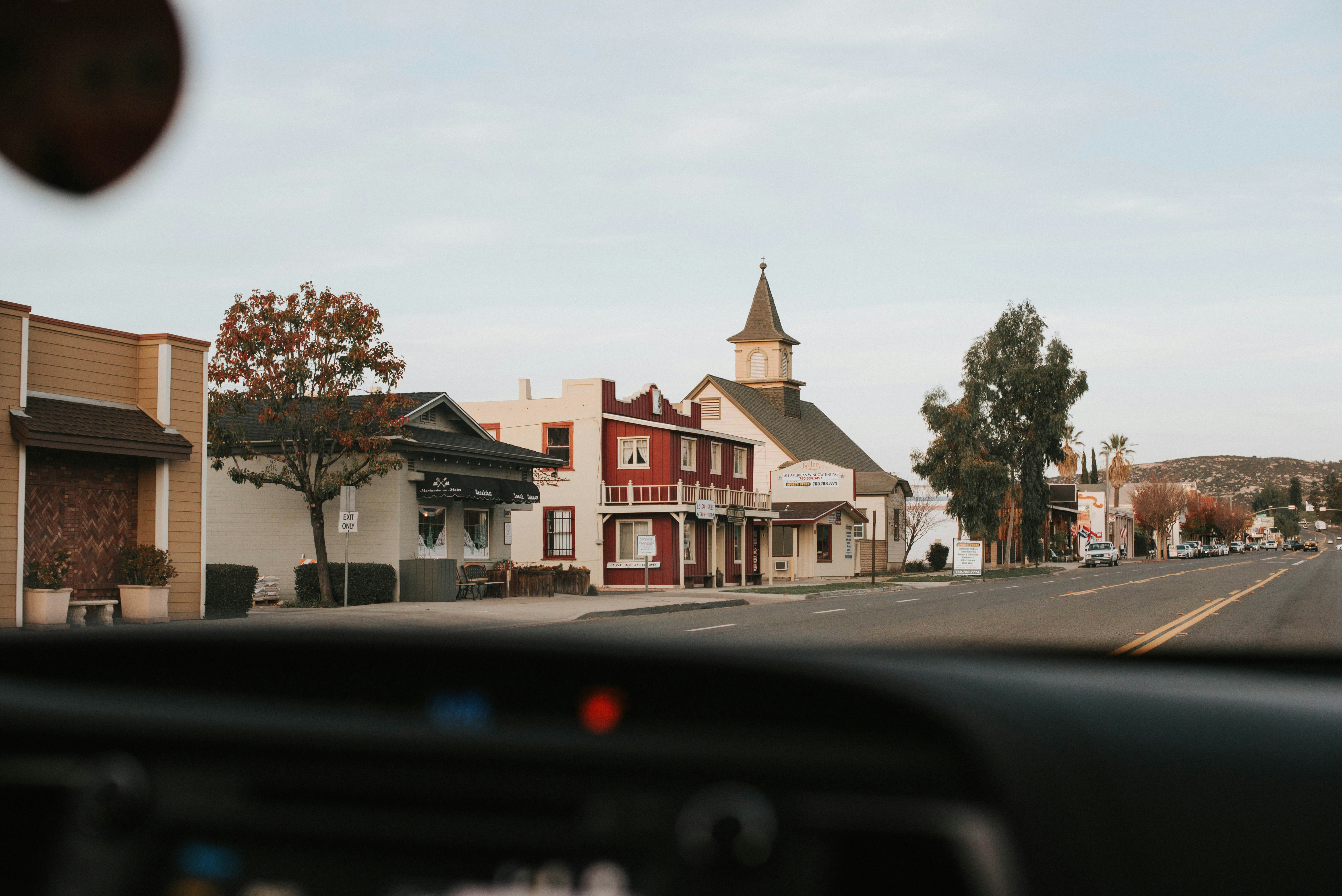 Quaint buildings line a peaceful street, showcasing classic architecture and autumn foliage. A church steeple adds a touch of historical charm.