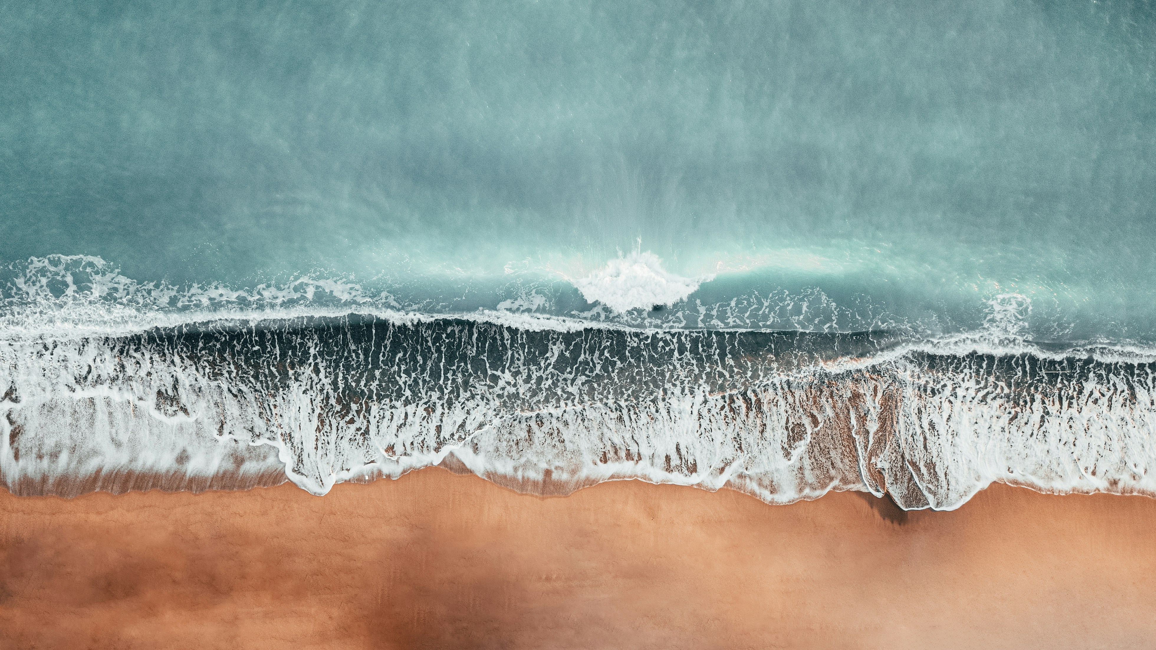 Aerial view capturing the dynamic interaction between ocean waves and sandy beach, showcasing the textures and colors of both elements.