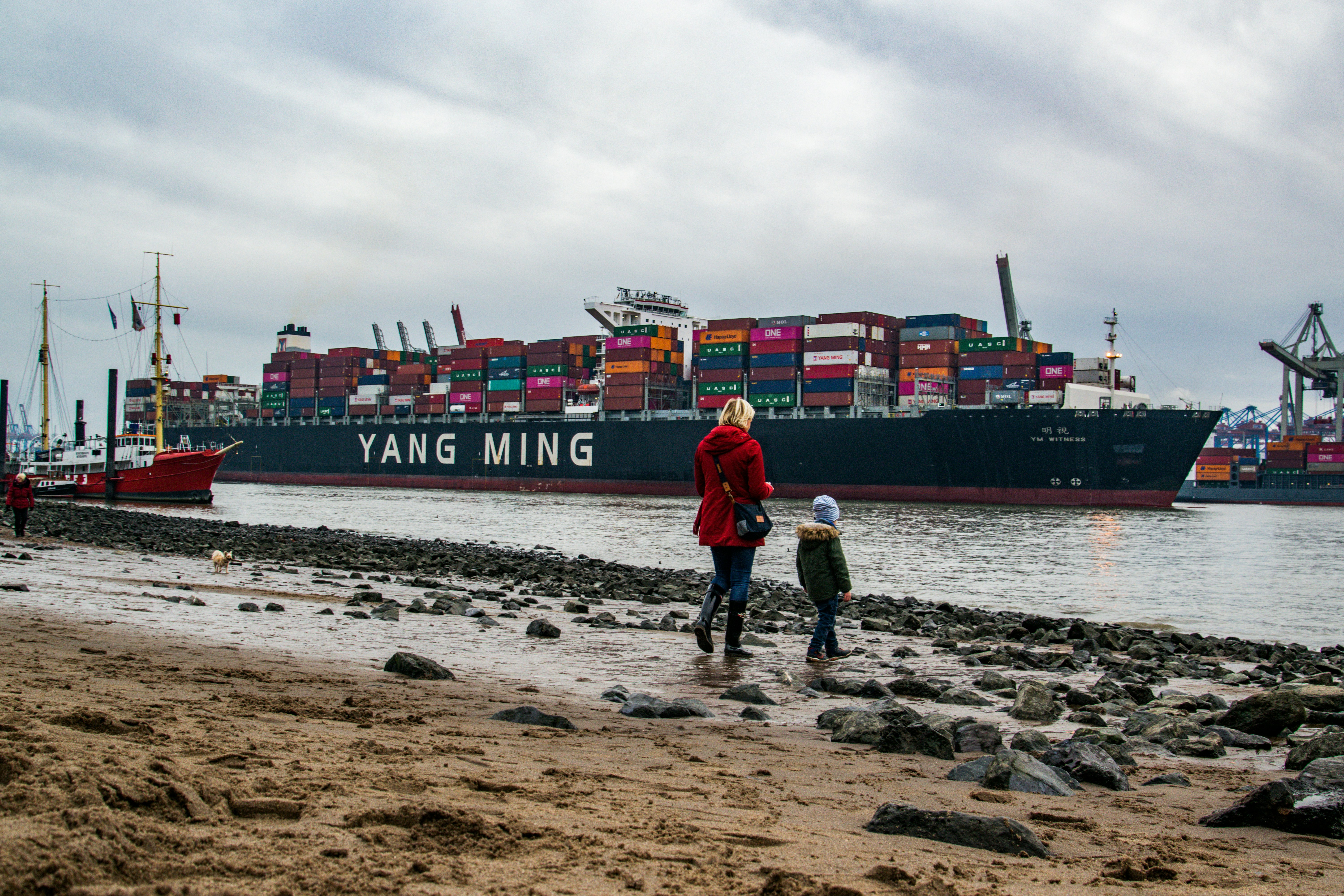 Large cargo ship navigating a bustling harbor with a cloudy sky overhead.