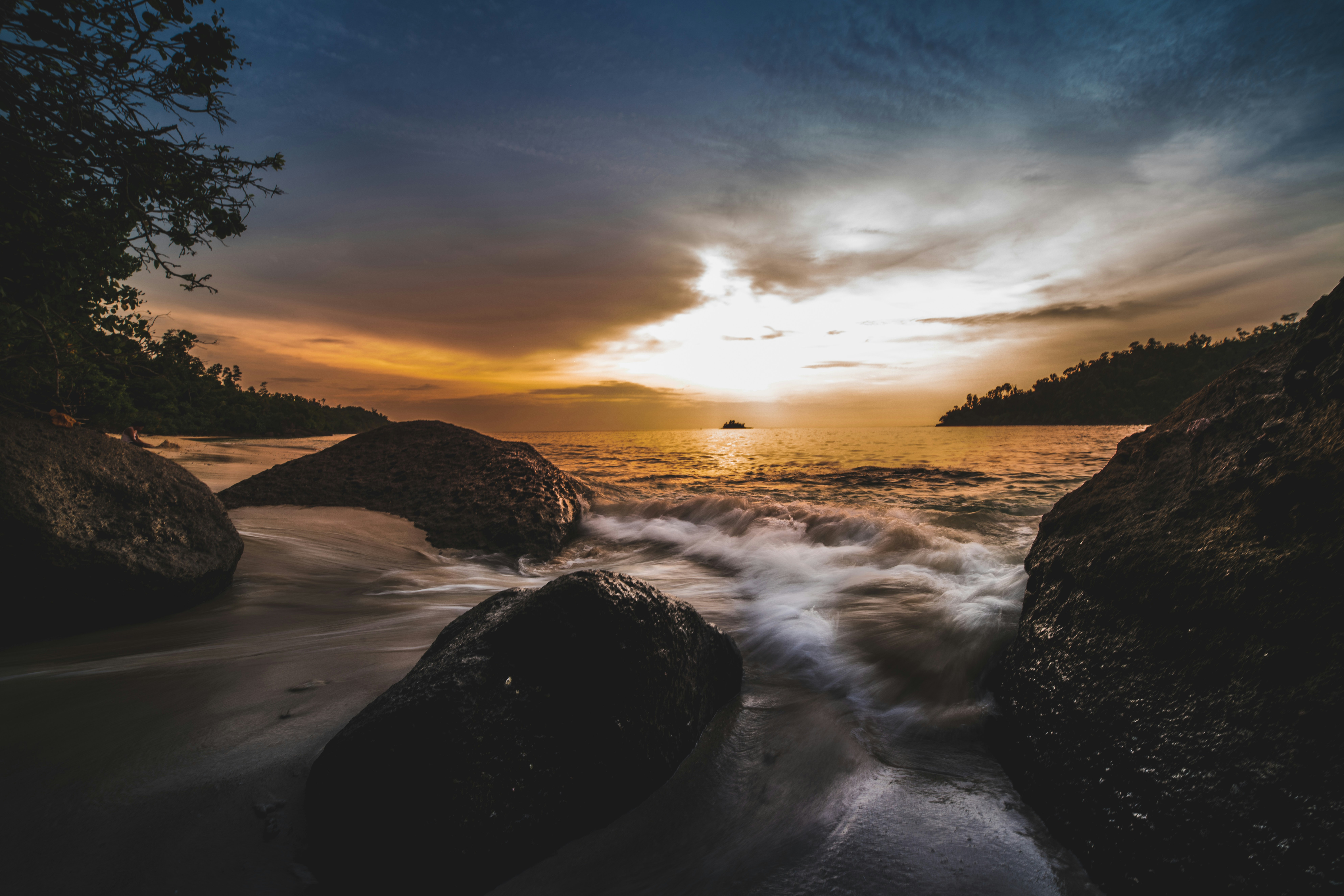 Waves gently wash over rocks under a vibrant sunset sky at a tranquil beach.