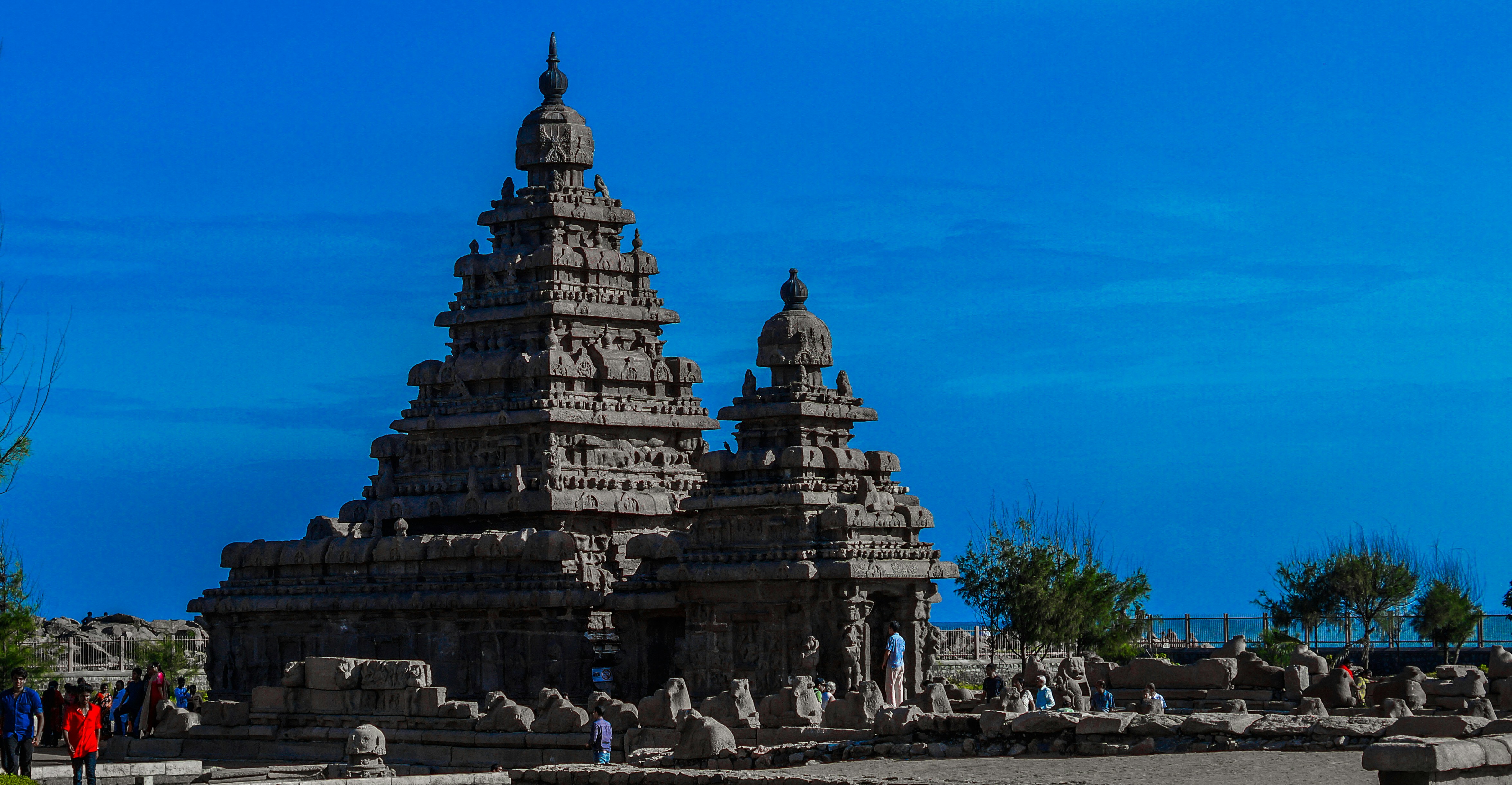 Intricate stone temple structure surrounded by visitors under a clear blue sky. The architectural details showcase historical artistry.
