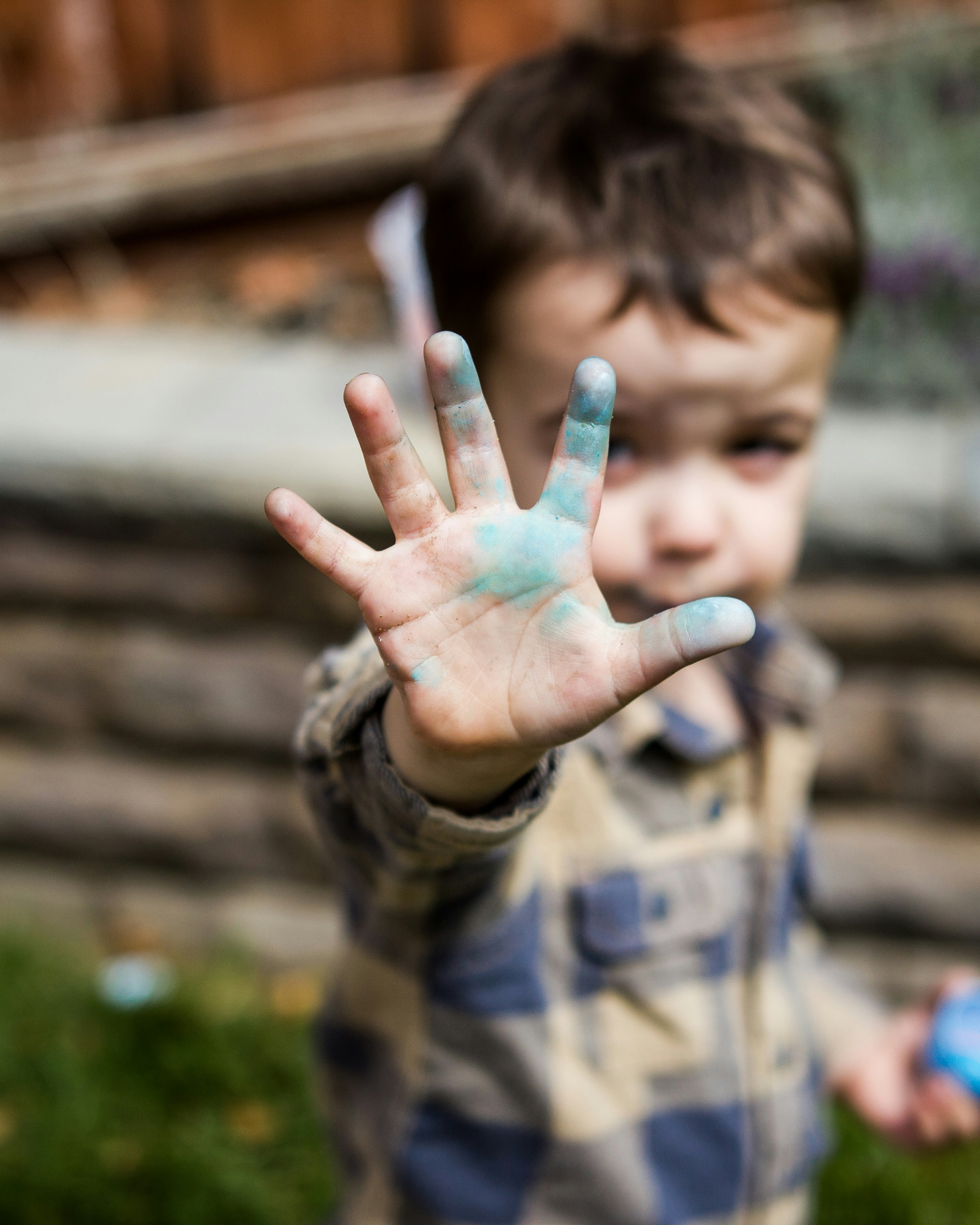 Child displaying a hand covered in blue paint, showcasing playful creativity in a vibrant outdoor setting.