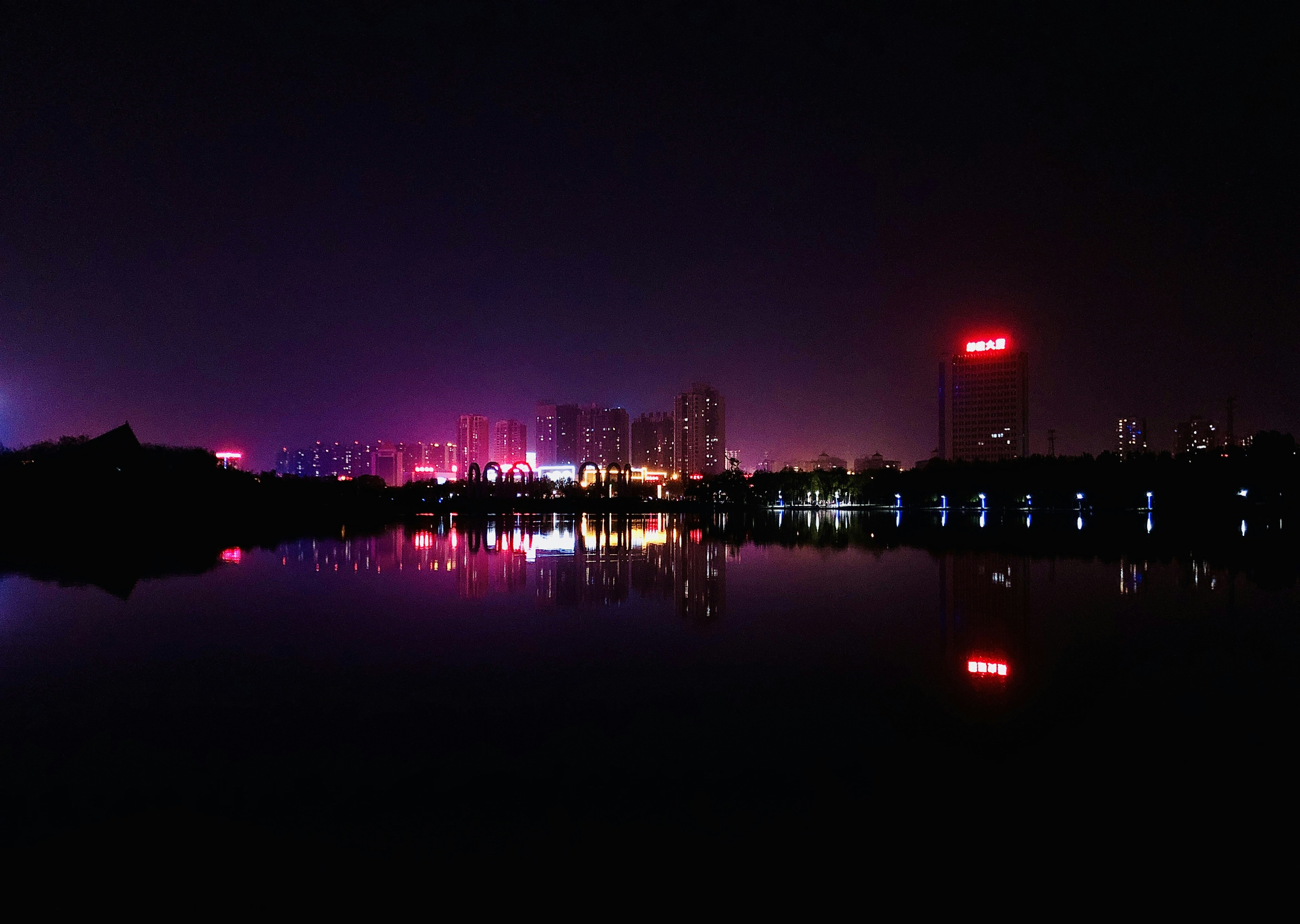 City skyline with vibrant neon lights mirrored in a calm lake at night.