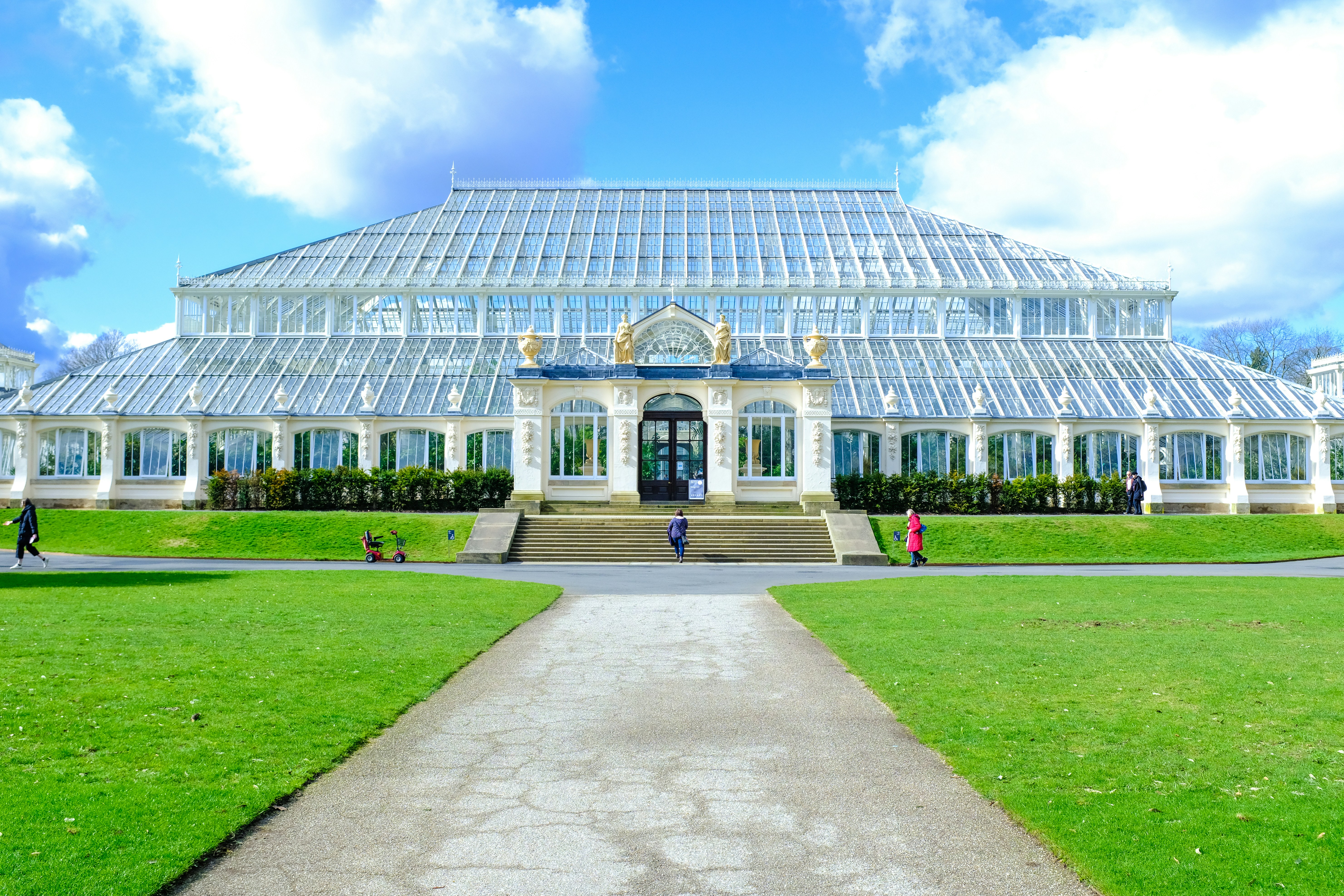 Grand glass conservatory with symmetrical design against a vibrant green lawn and blue sky.