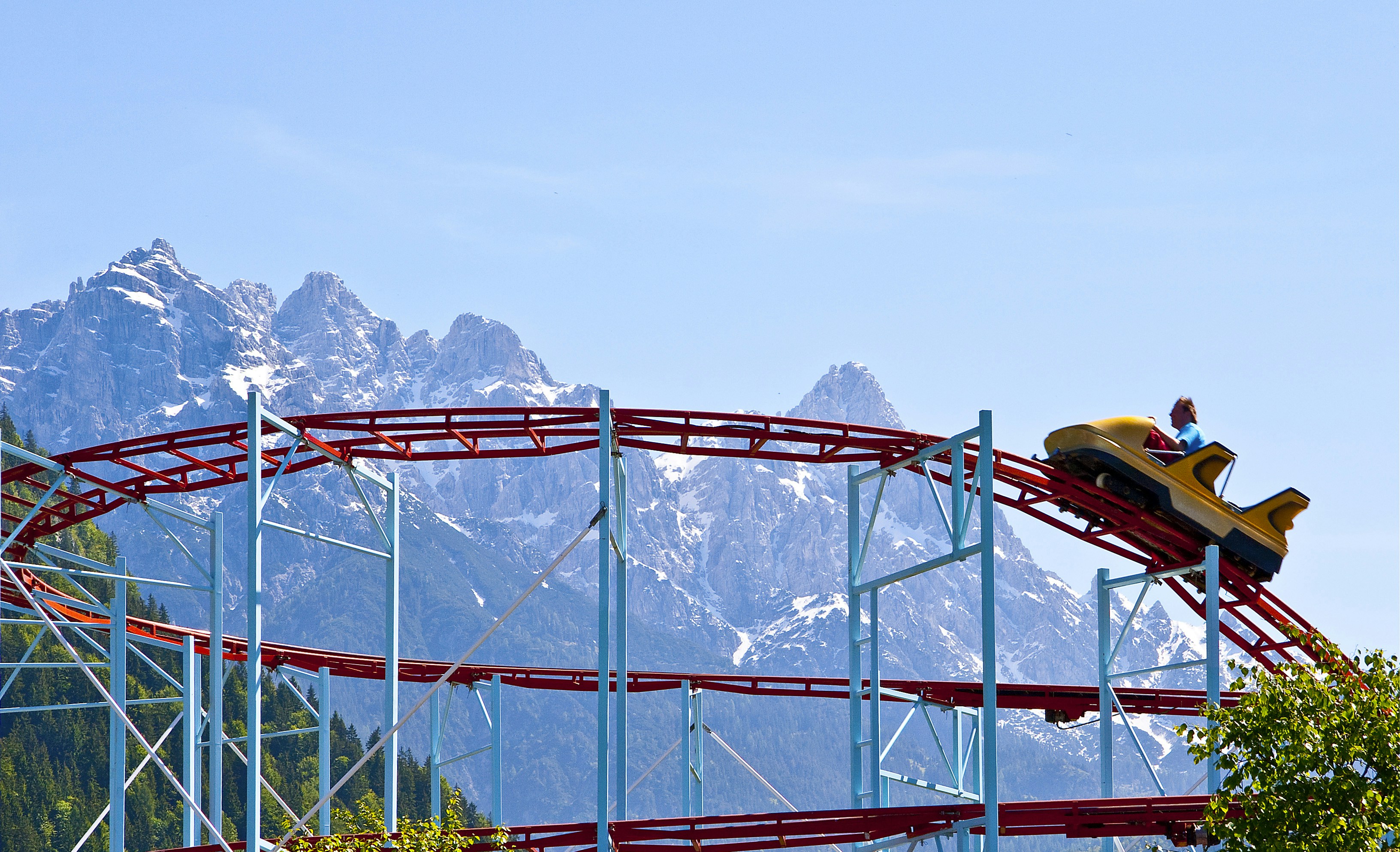 A roller coaster ascends against snow-capped mountains, showcasing the thrill of amusement parks amidst nature's grandeur.