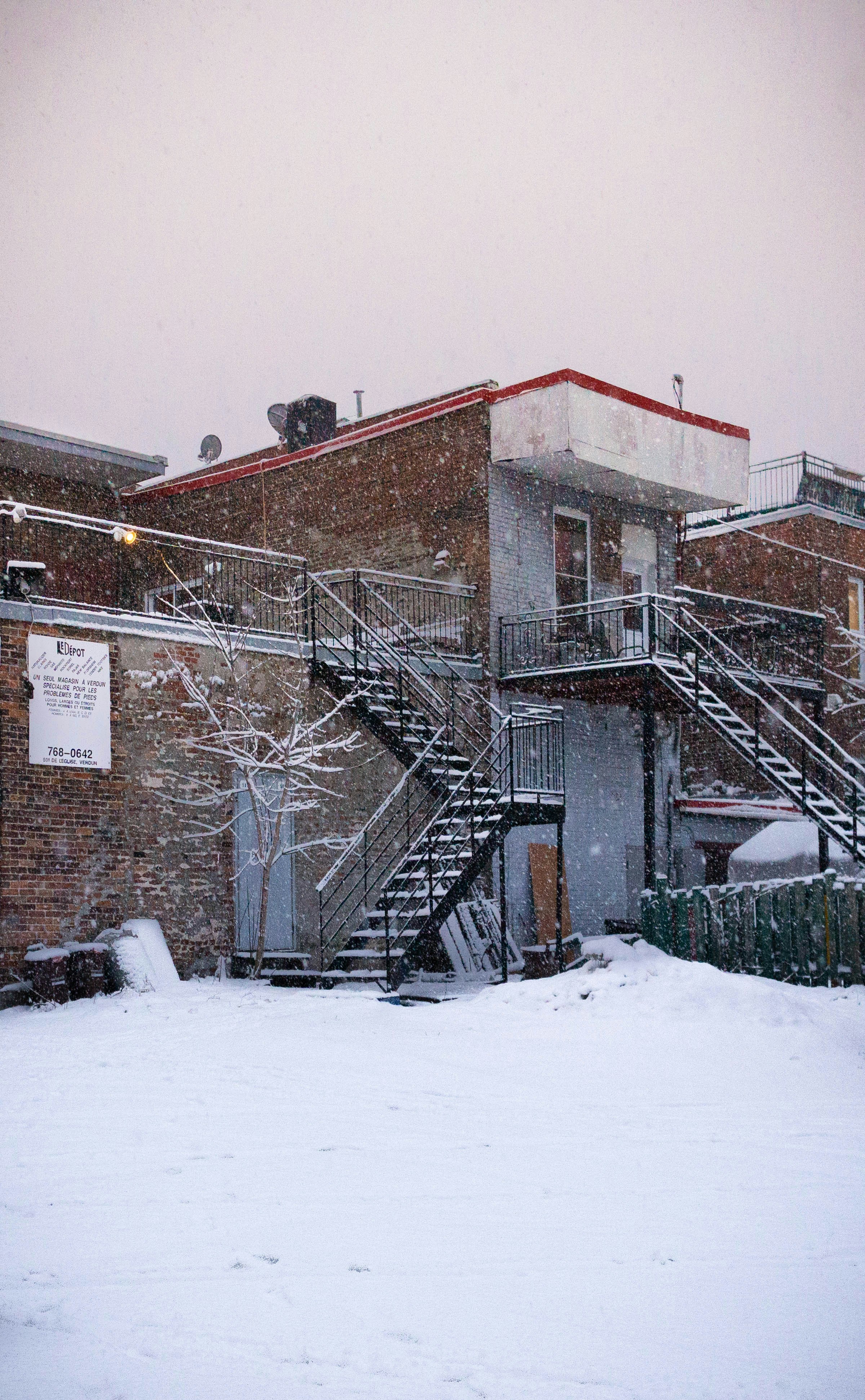 Snow-covered building with a staircase and signage, enveloped in a gentle snowfall during twilight.