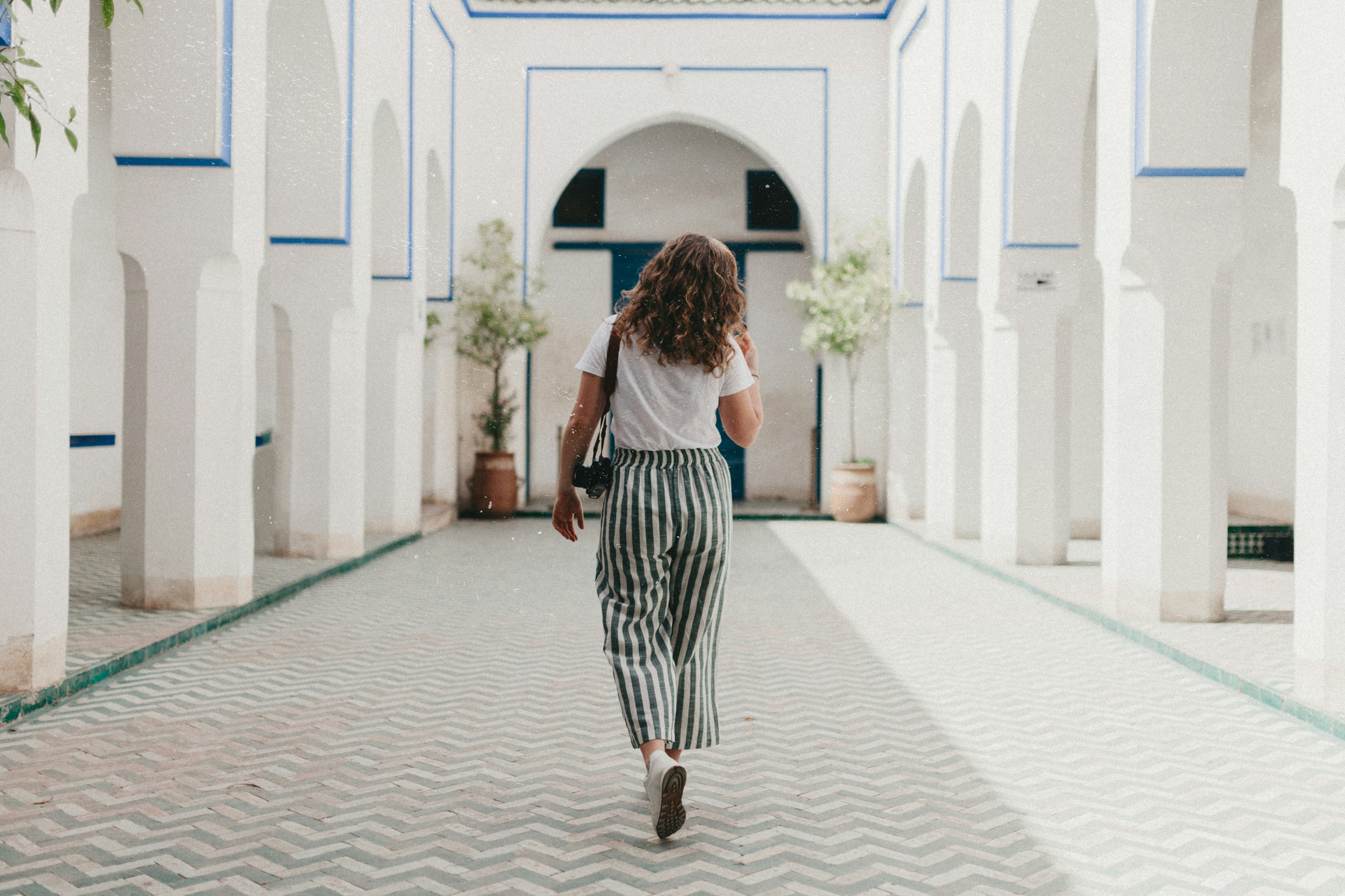 Person walking through a bright, patterned courtyard with white arches and blue accents.