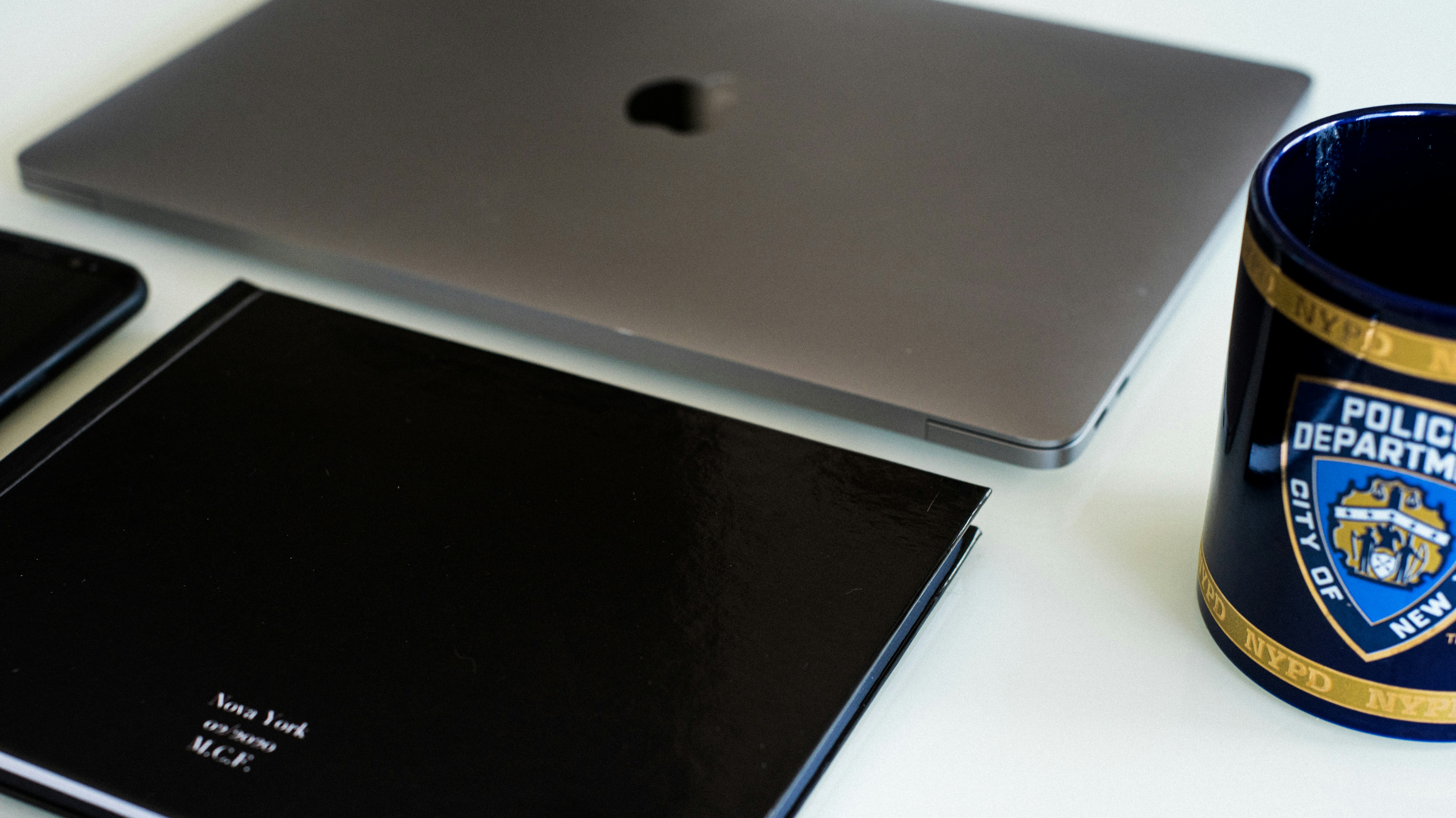 Sleek laptop and notebook with a police-themed mug on a white desk.