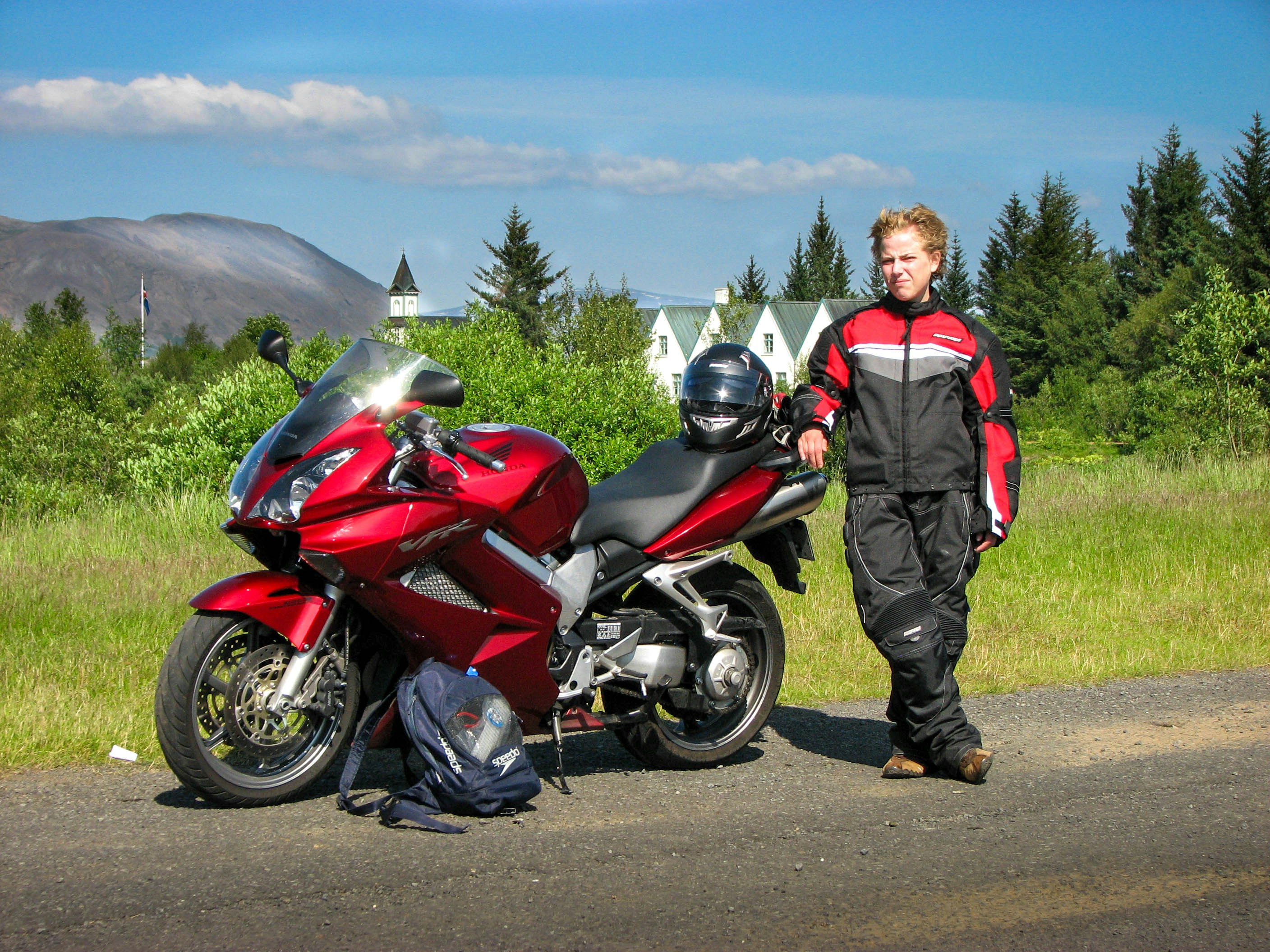 Crimson Ride: Rider and Red Sport-Touring Beside a Sunlit Nordic Field