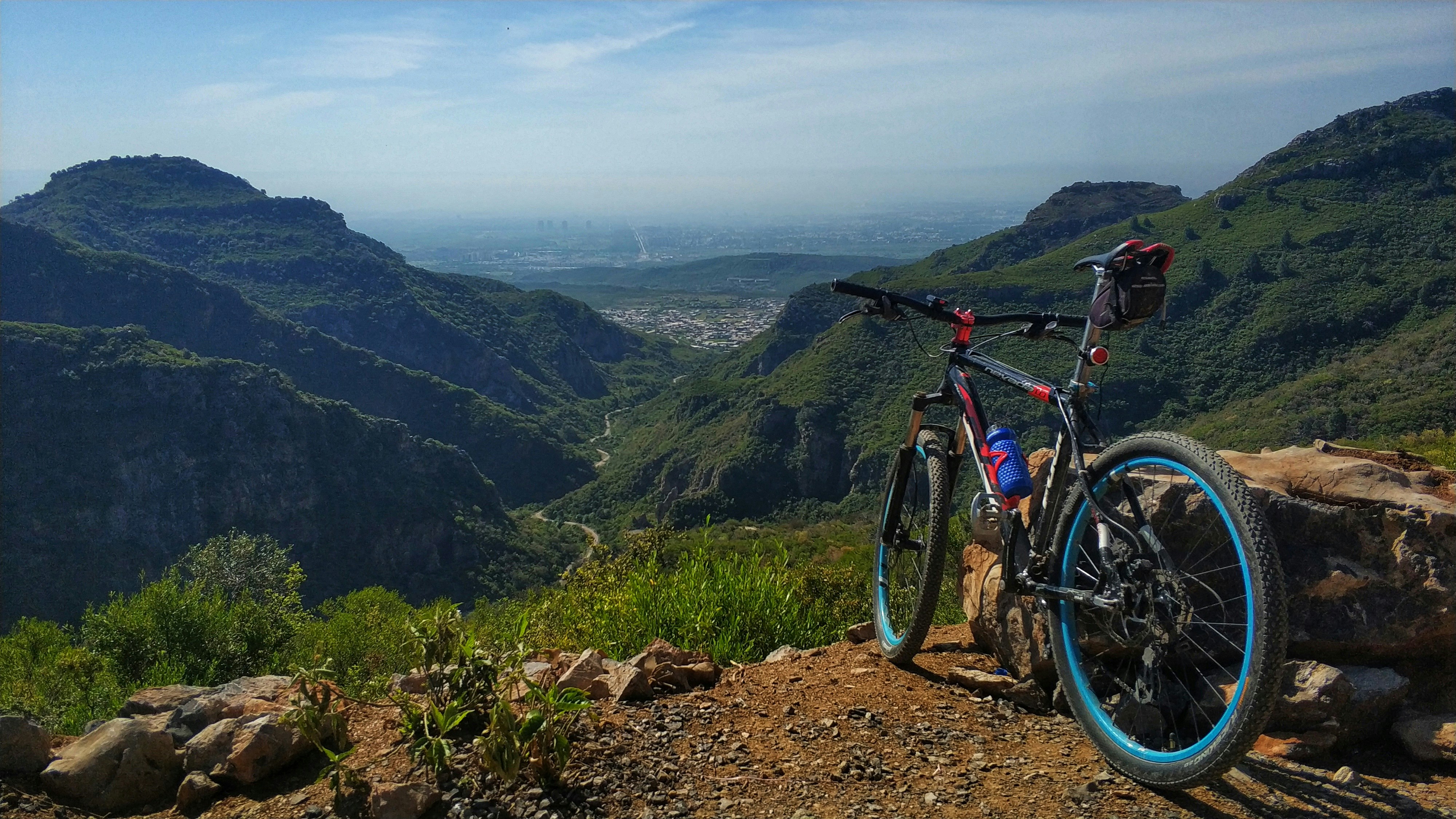 Blue and black mountain bike on a dirt road overlooking a vast valley under a clear sky.
