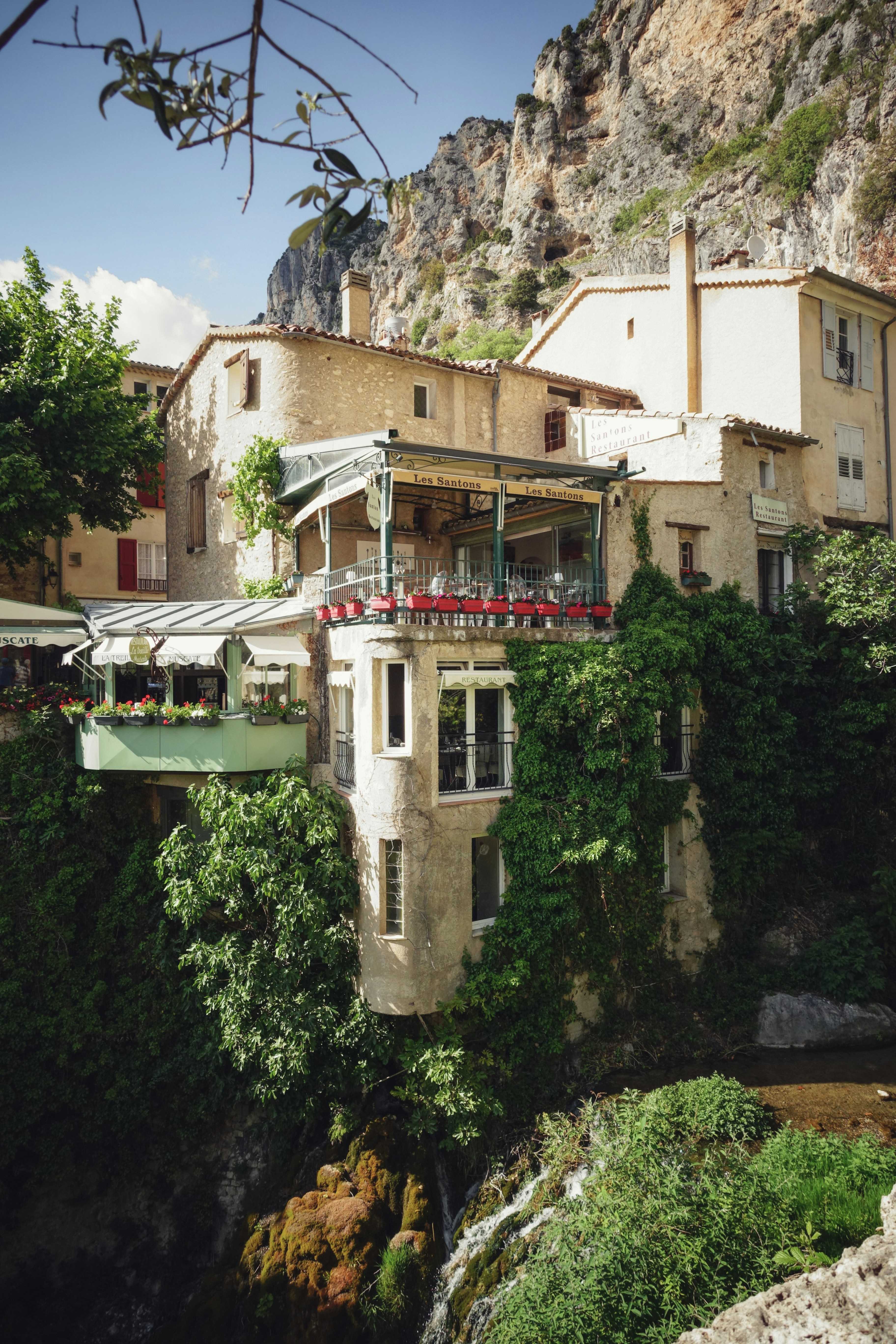 Charming restaurant perched on a cliffside, surrounded by lush greenery and cascading water. The rustic architecture blends harmoniously with the natural landscape.