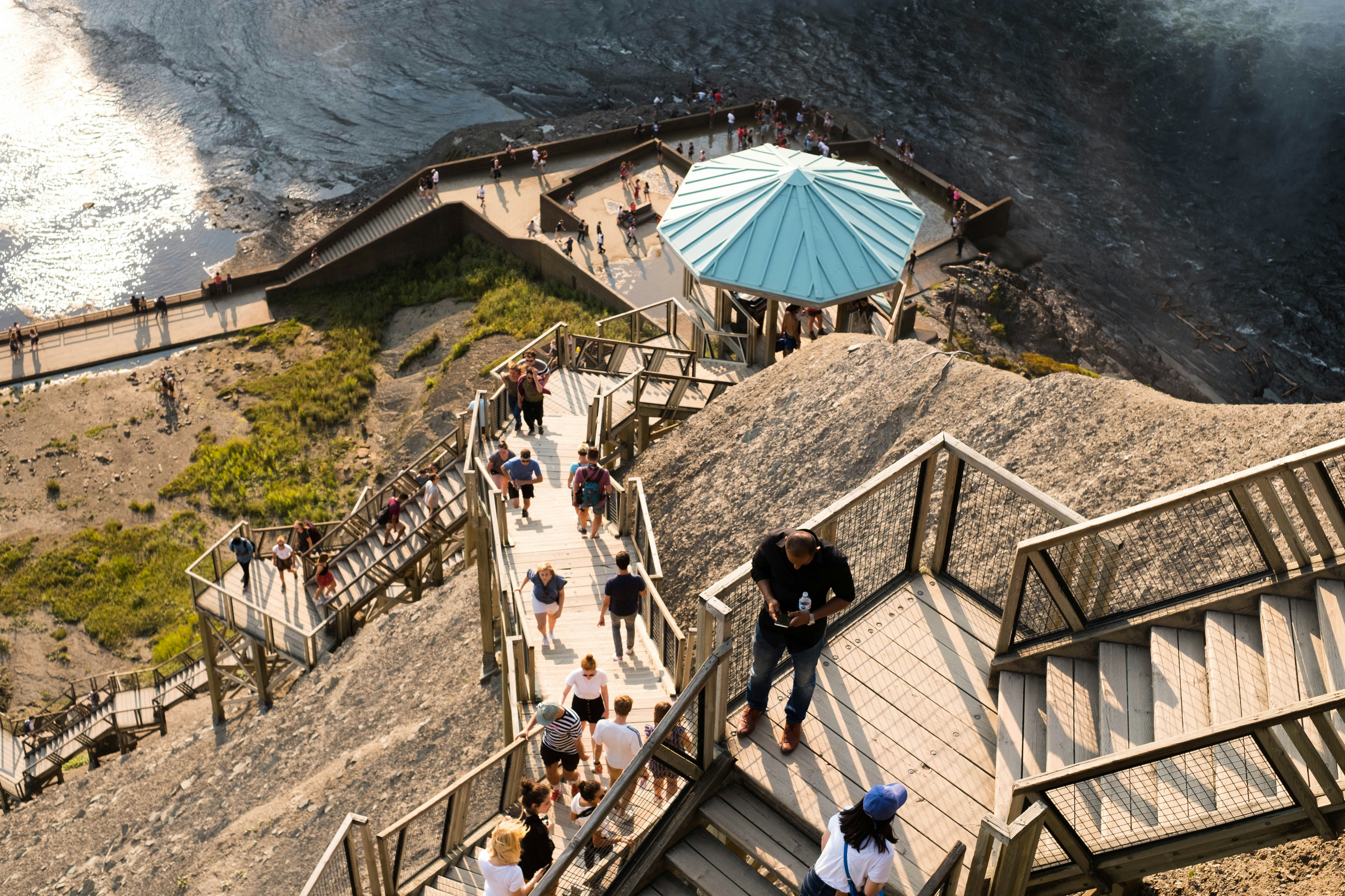 Visitors on wooden stairs by a rocky cliff overlooking a shimmering river.