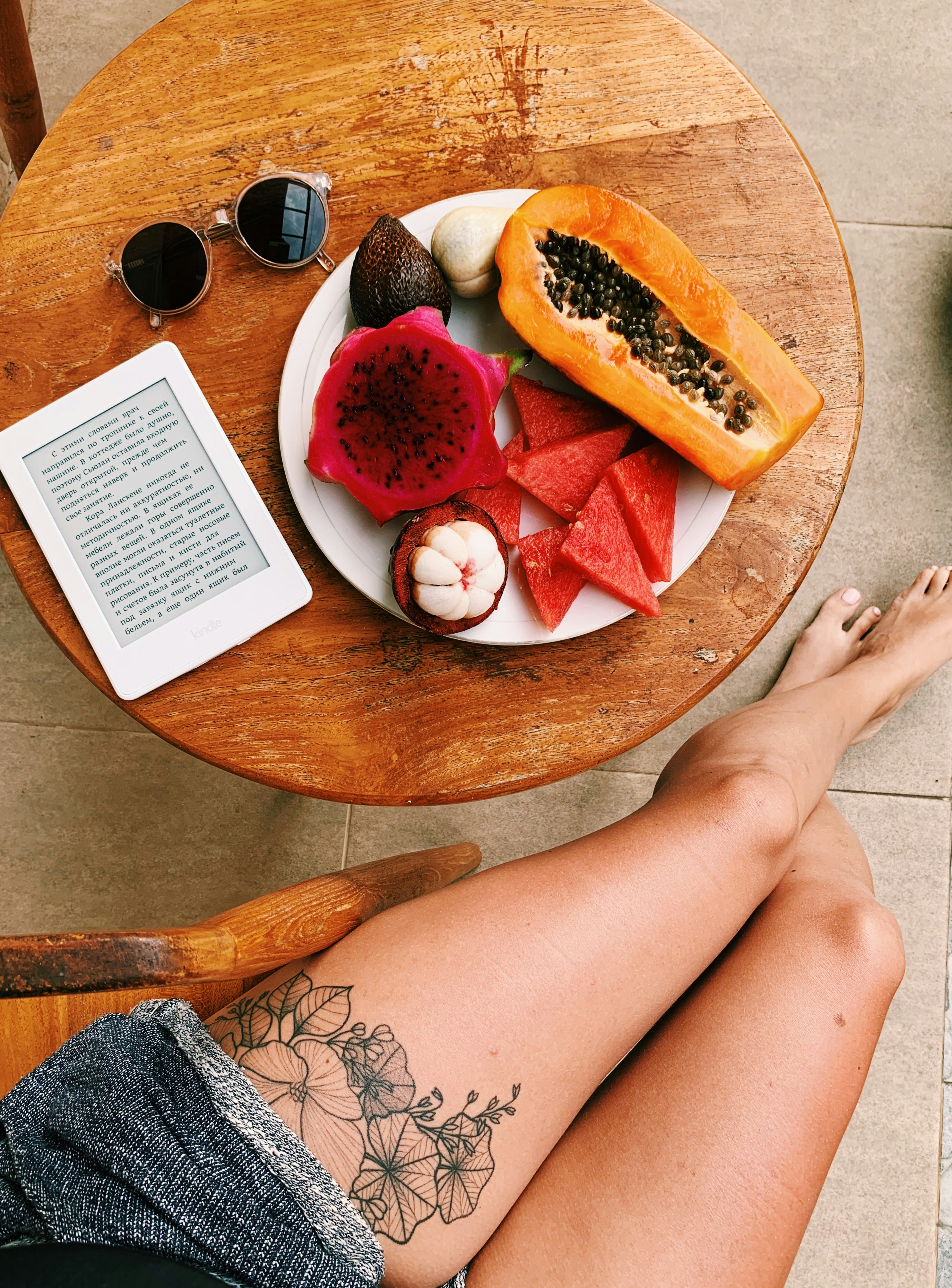 Sunlit tropical fruit platter framed by a tattooed leg