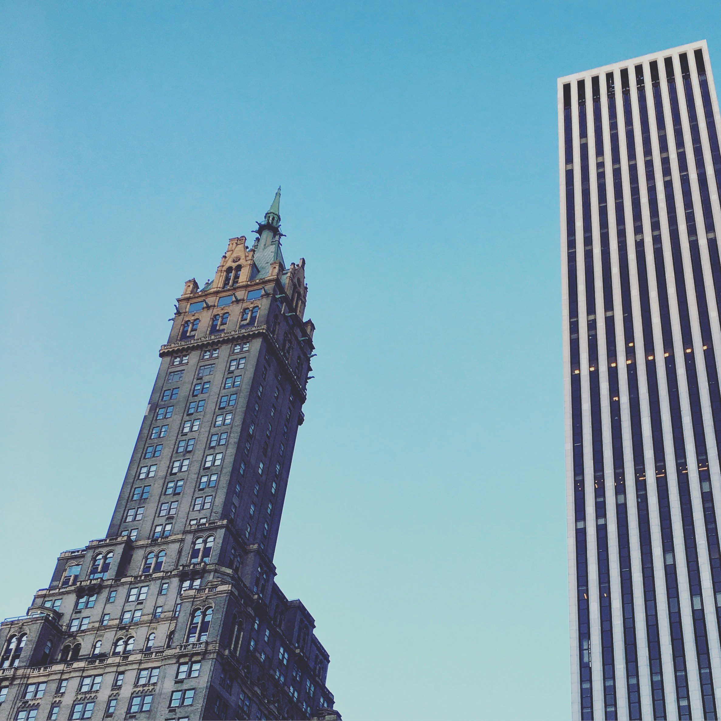 Historic skyscraper juxtaposed against a modern glass building under a clear blue sky.