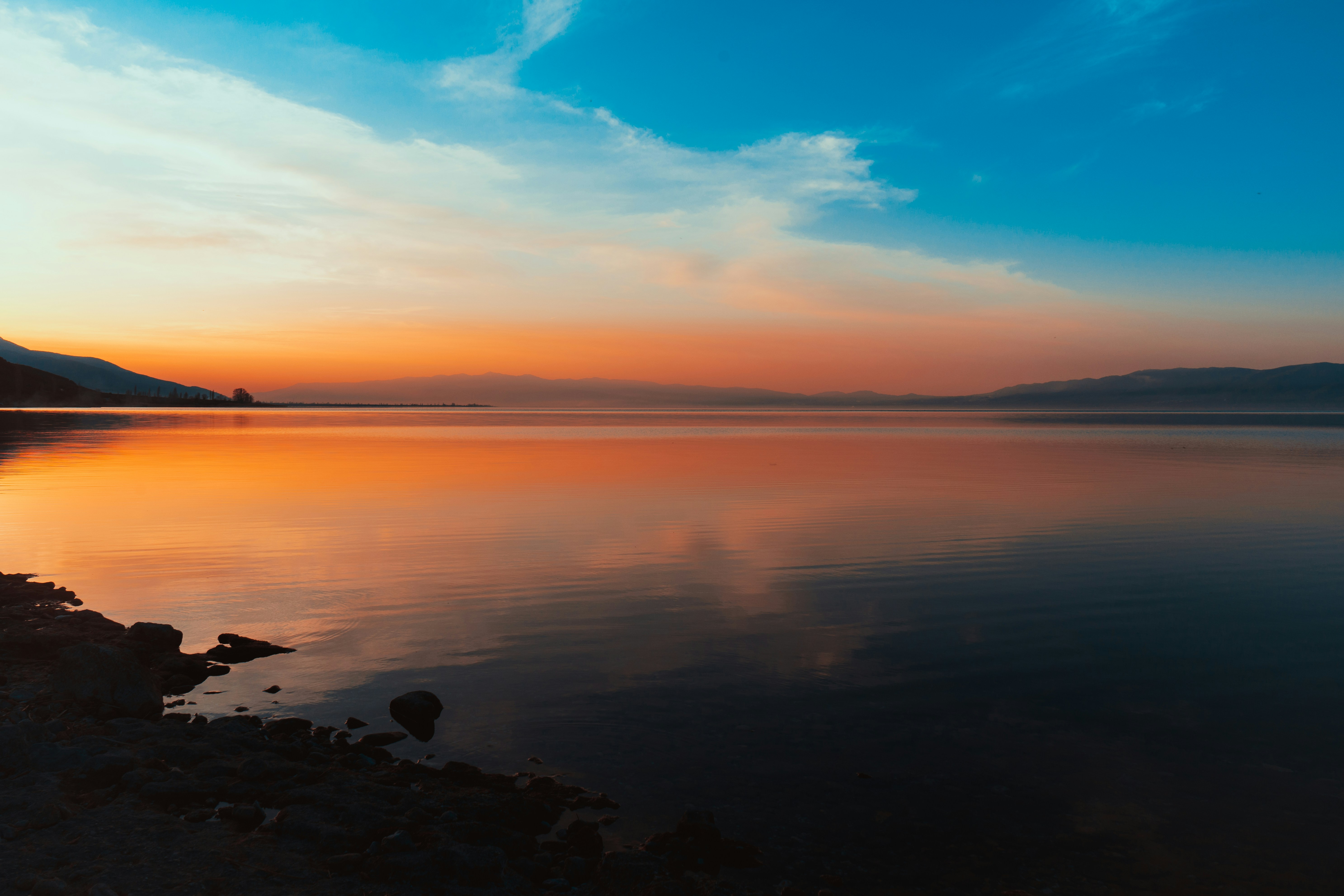 Vibrant sunset over a tranquil lake, with orange and blue reflections on the water.