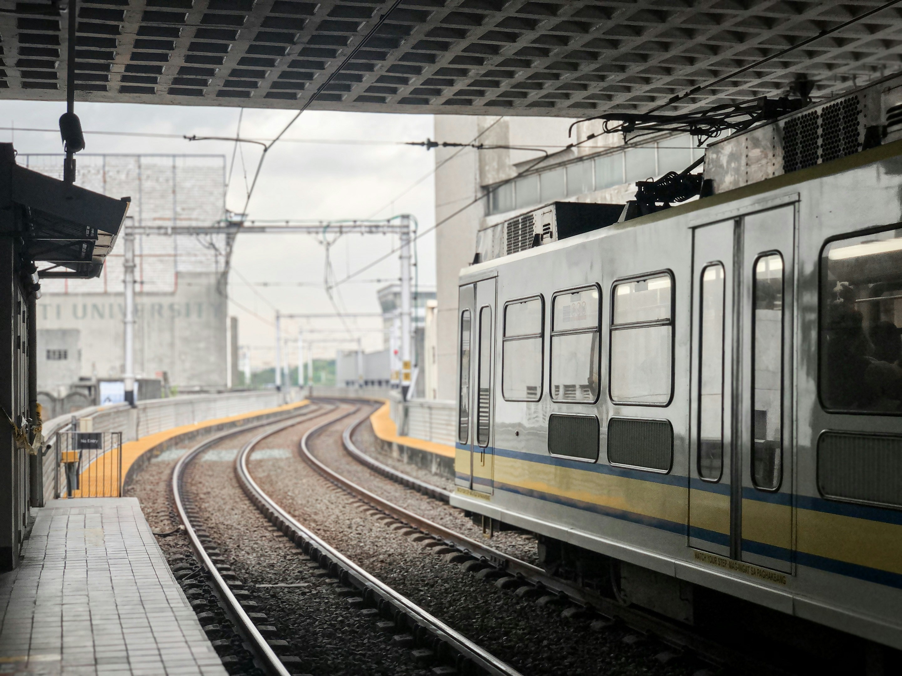 Train approaching on a curved track under a covered station platform.