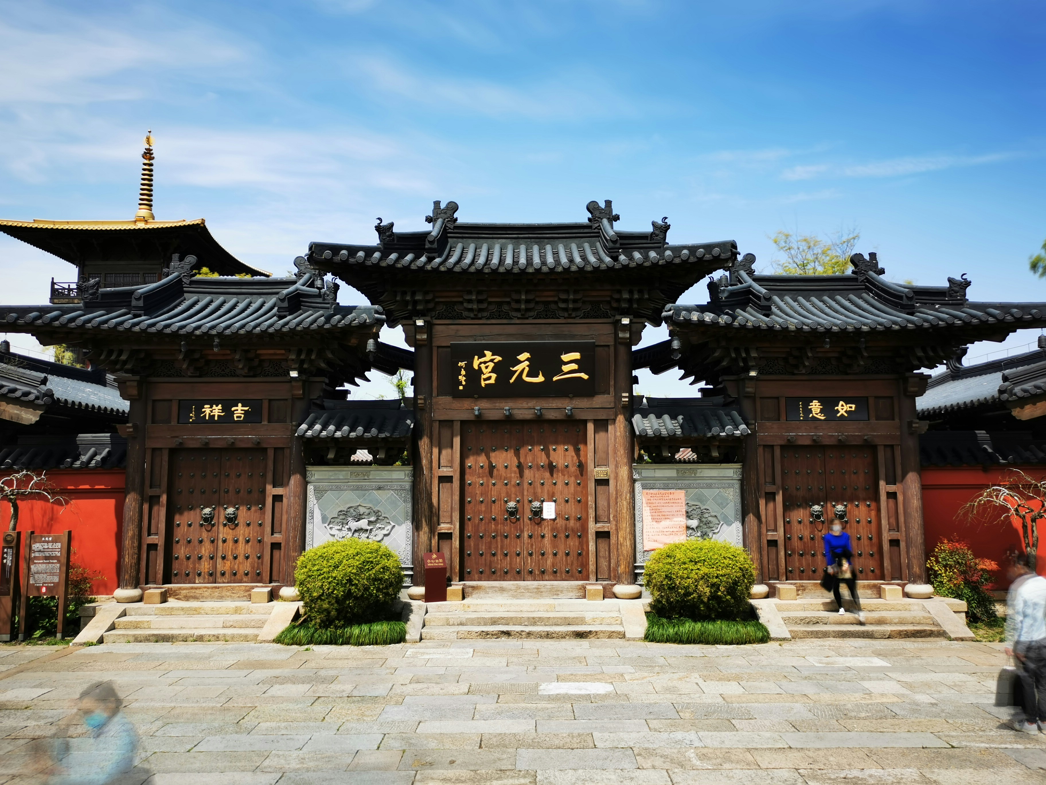 Historic temple entrance showcasing intricate wooden architecture and ornate doors, framed by lush greenery.