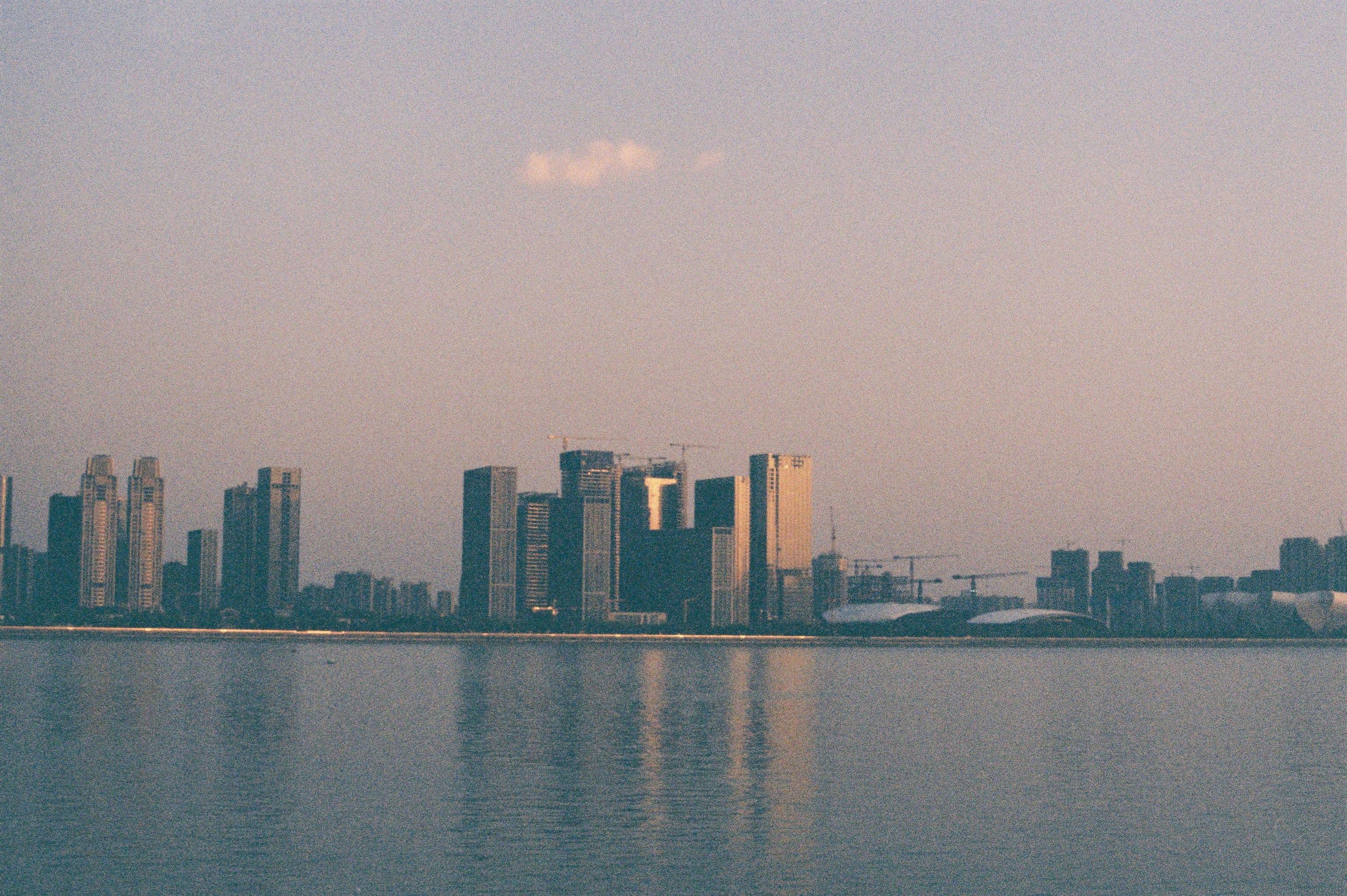 Modern skyline reflecting in calm waters during twilight, showcasing architectural diversity and urban life.