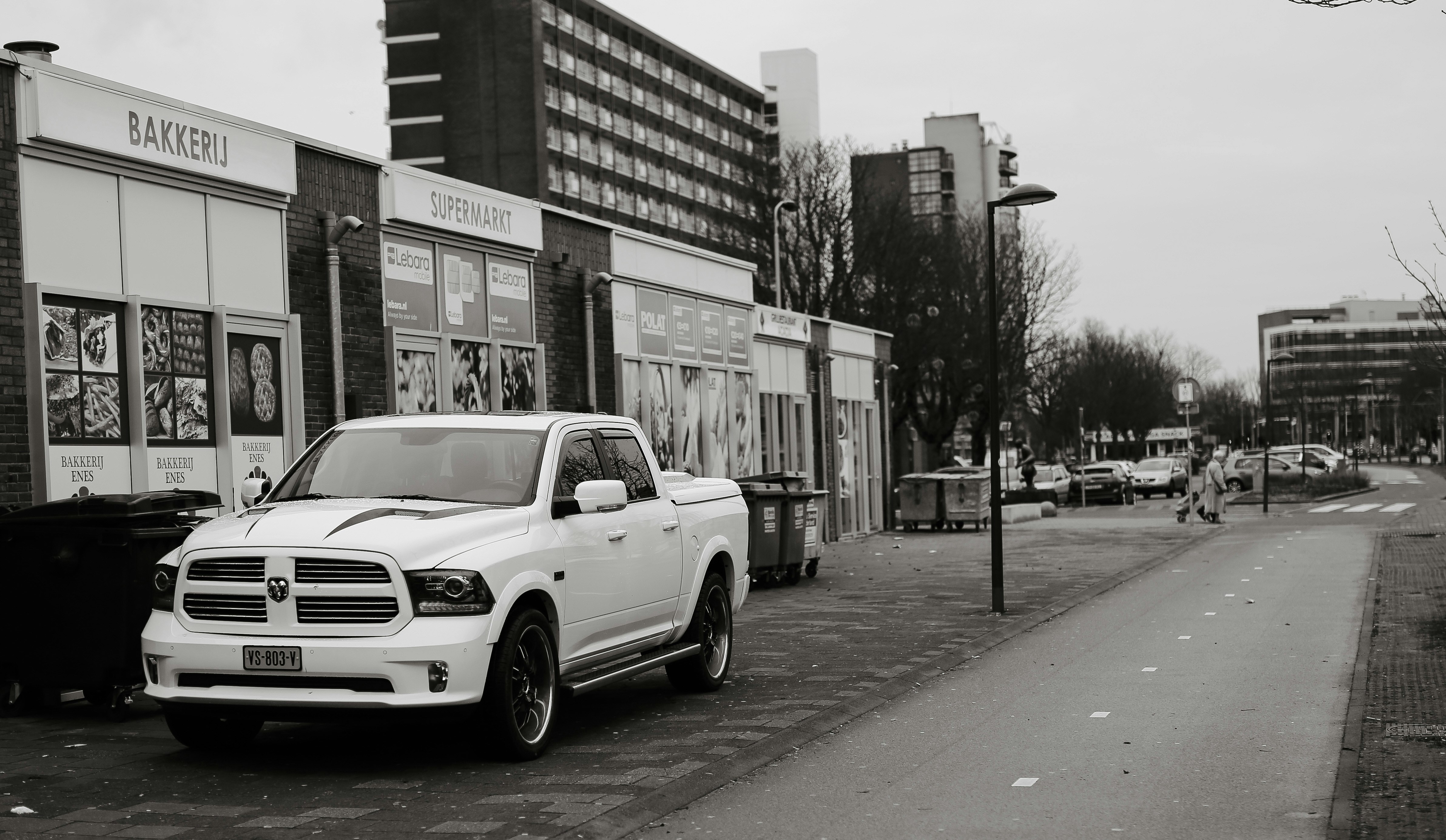 White pickup at the storefront row under a subdued urban sky