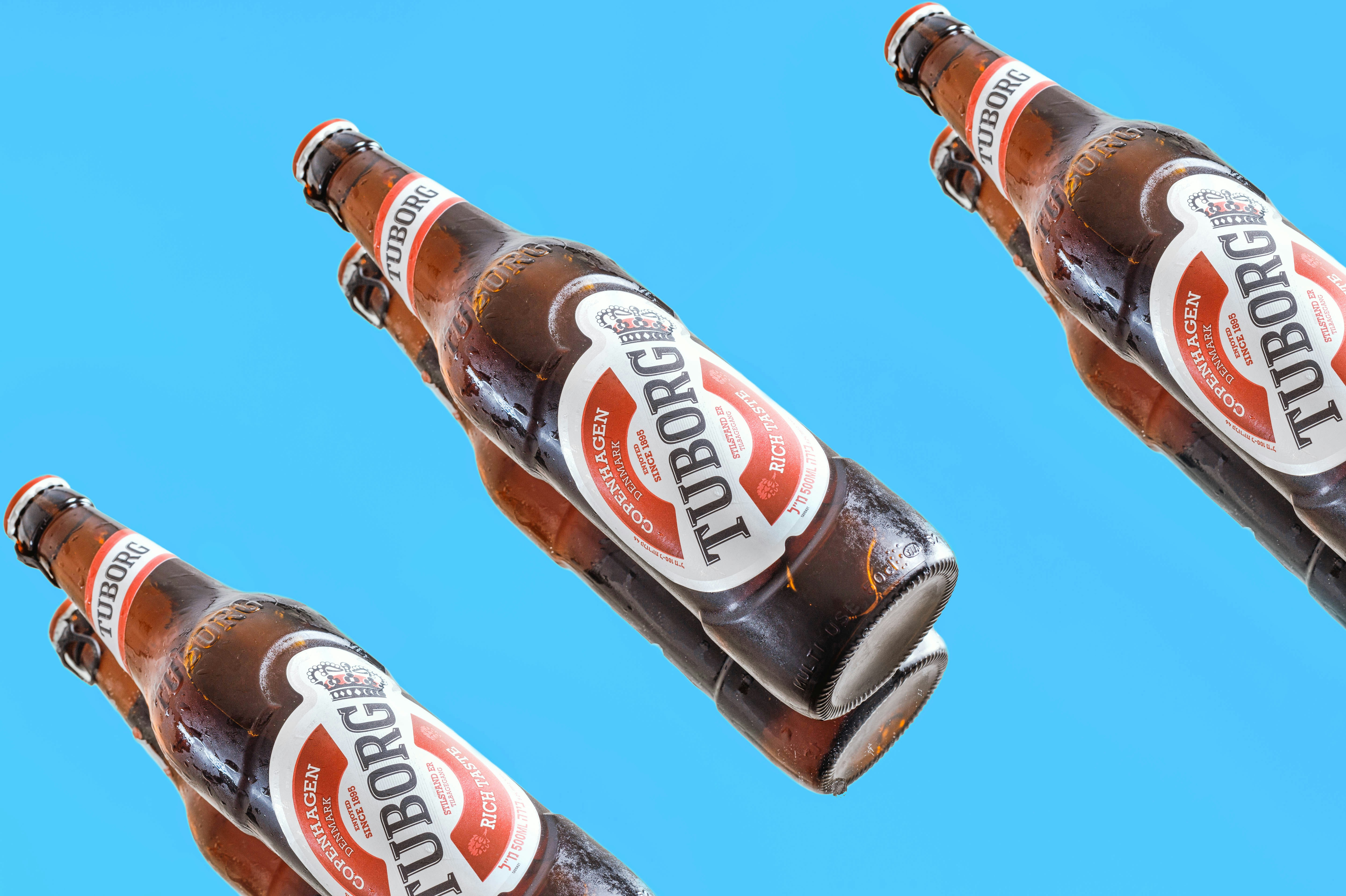 Three frosty Tuborg beer bottles arranged against a vibrant blue backdrop, showcasing their refreshing appeal.