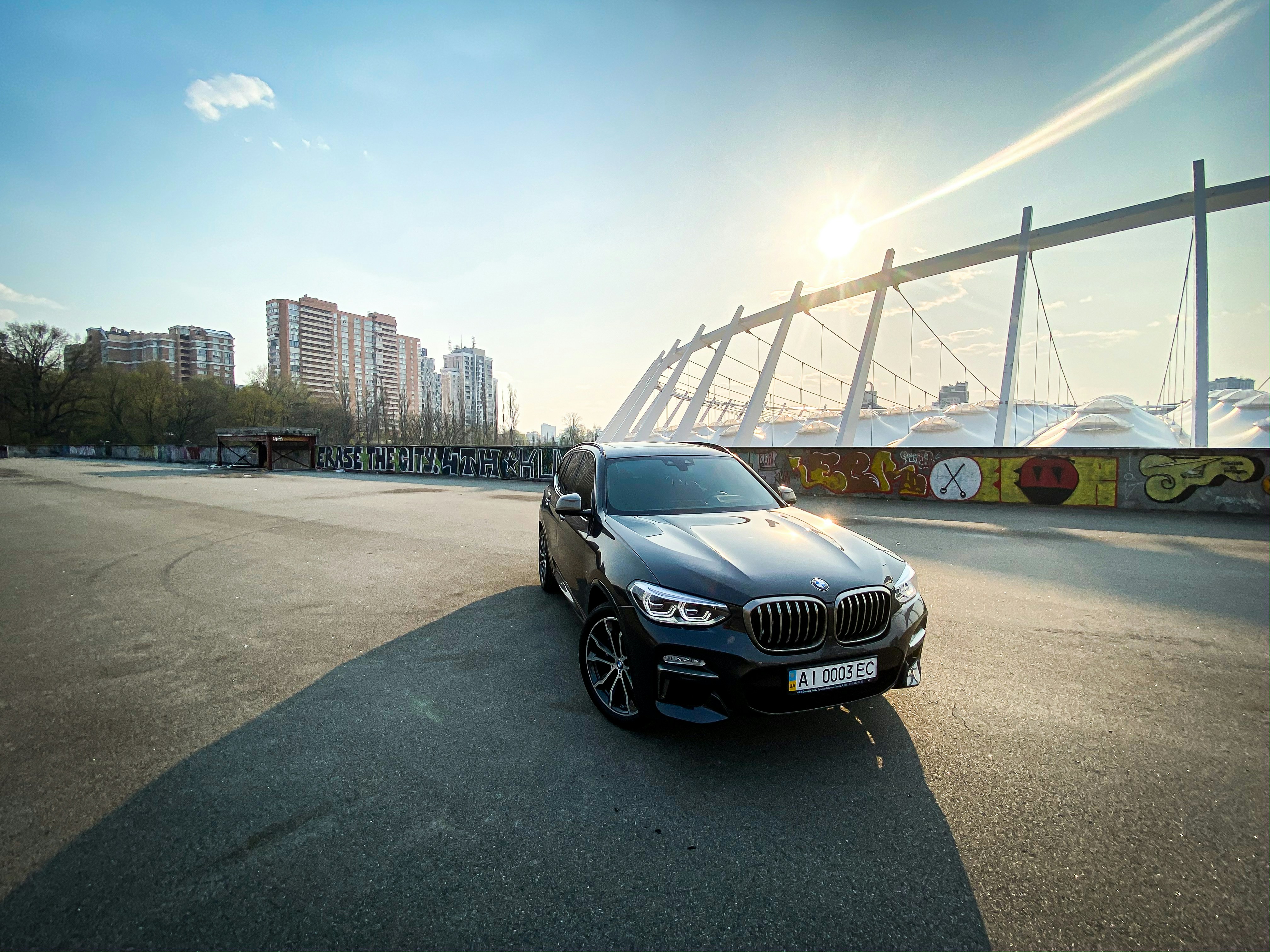 Sunlit Stance: BMW Anchored Against a Graffiti-Washed Riverside