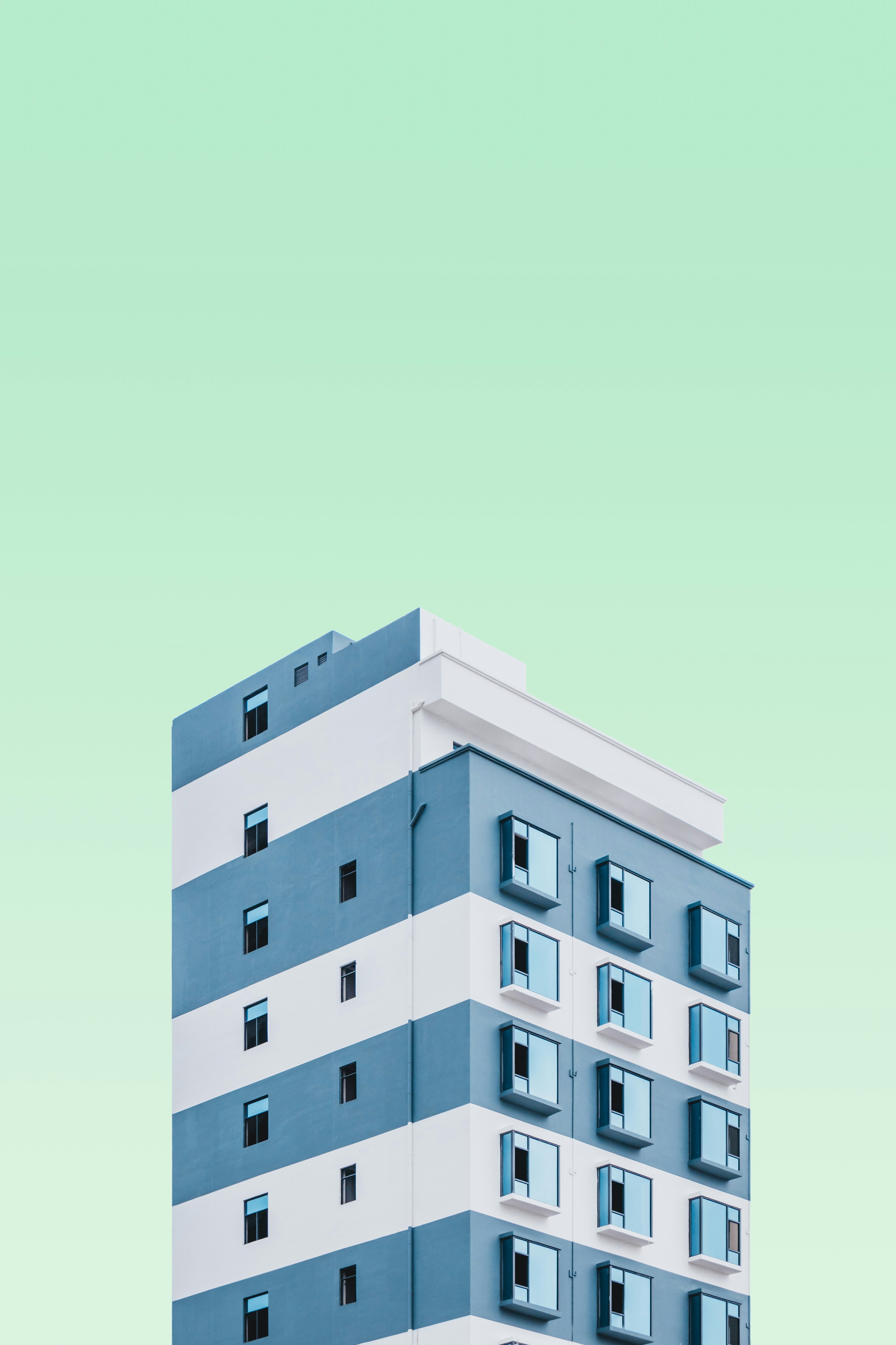 A modern building with a striking blue and white facade, featuring geometric patterns and multiple windows against a soft green background.