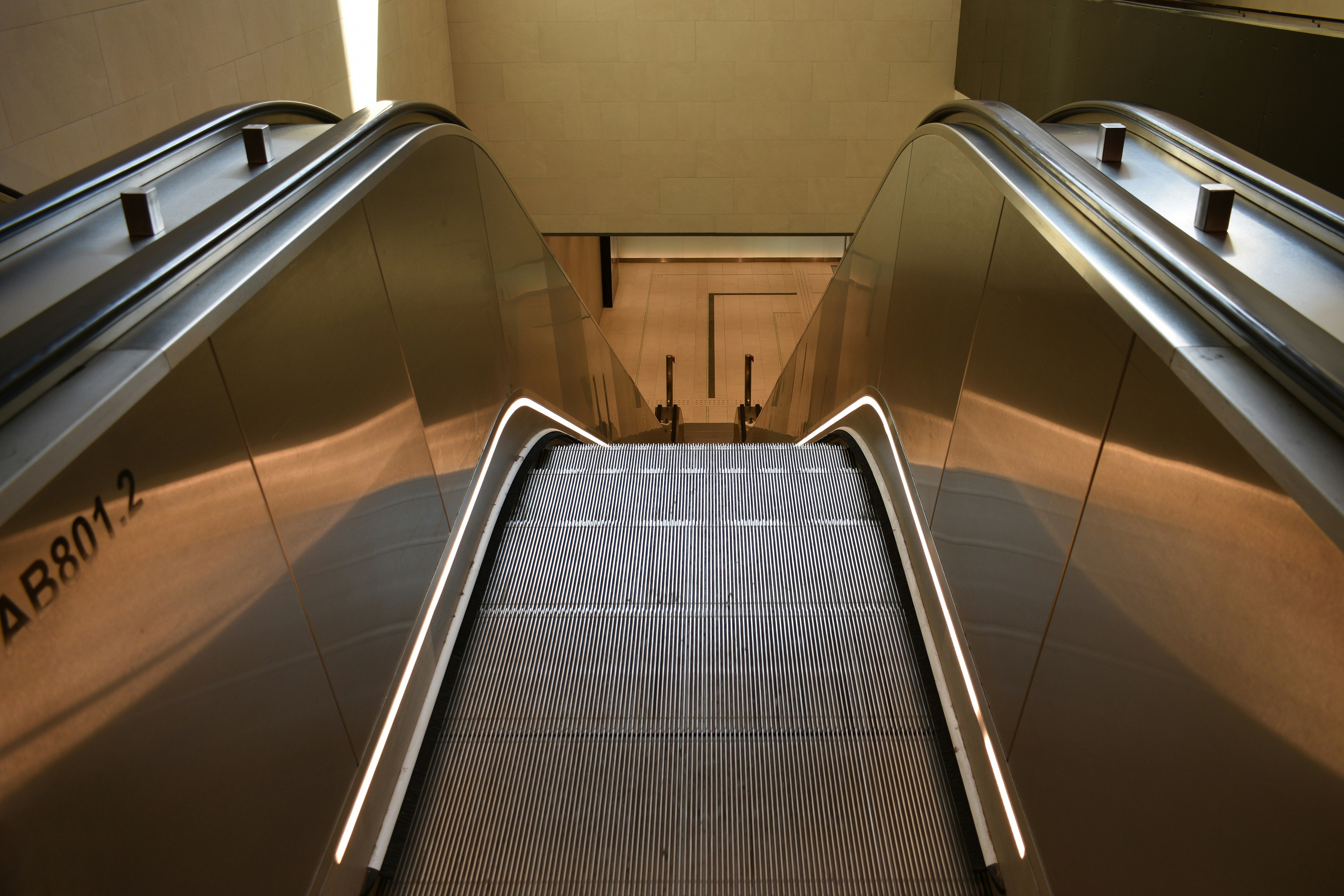 Escalator descending into a well-lit modern space, emphasizing sleek lines and reflective surfaces.
