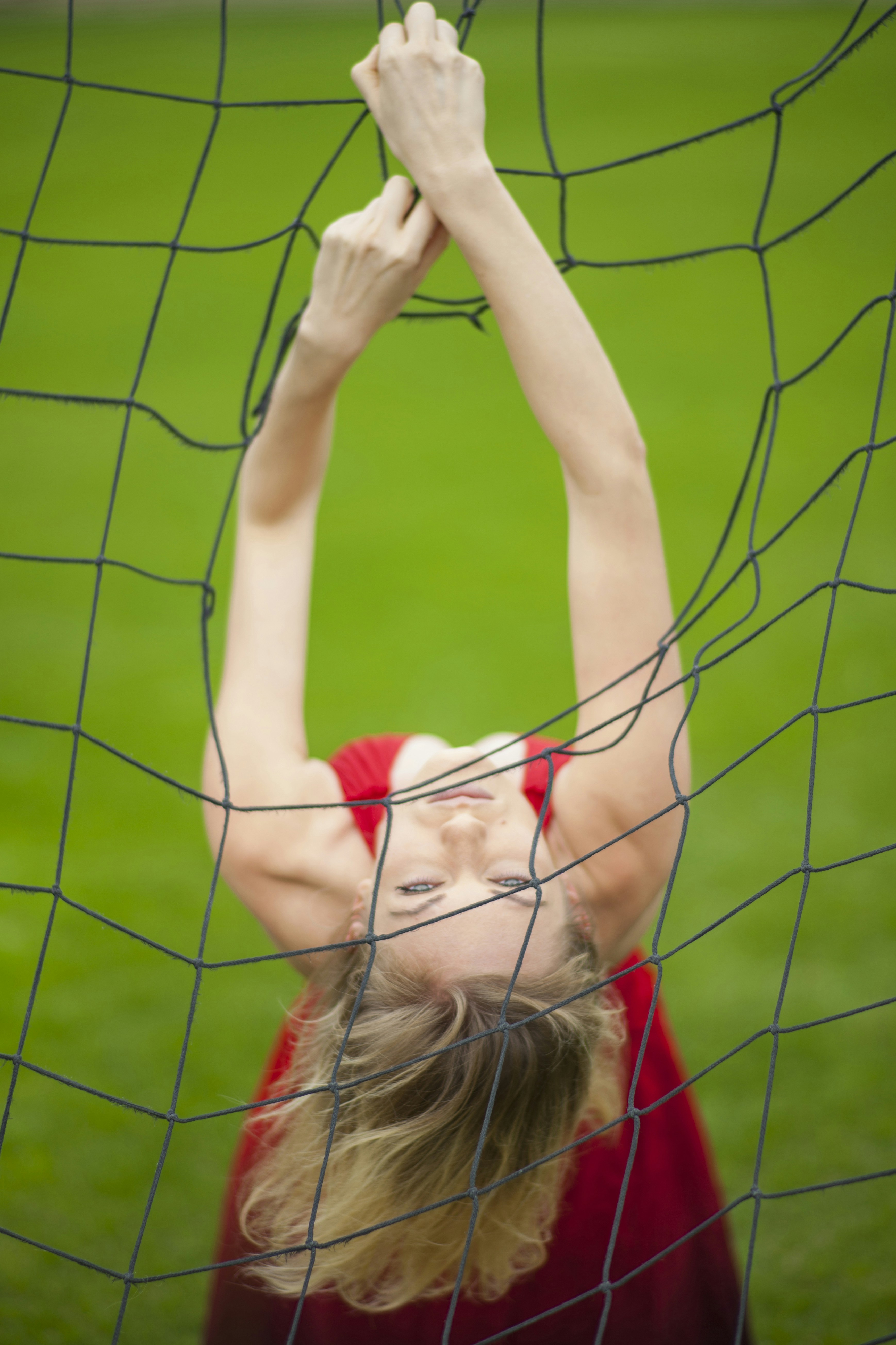 Upside-Down Play: A Girl Clings to the Soccer Net on a Lush Green Field