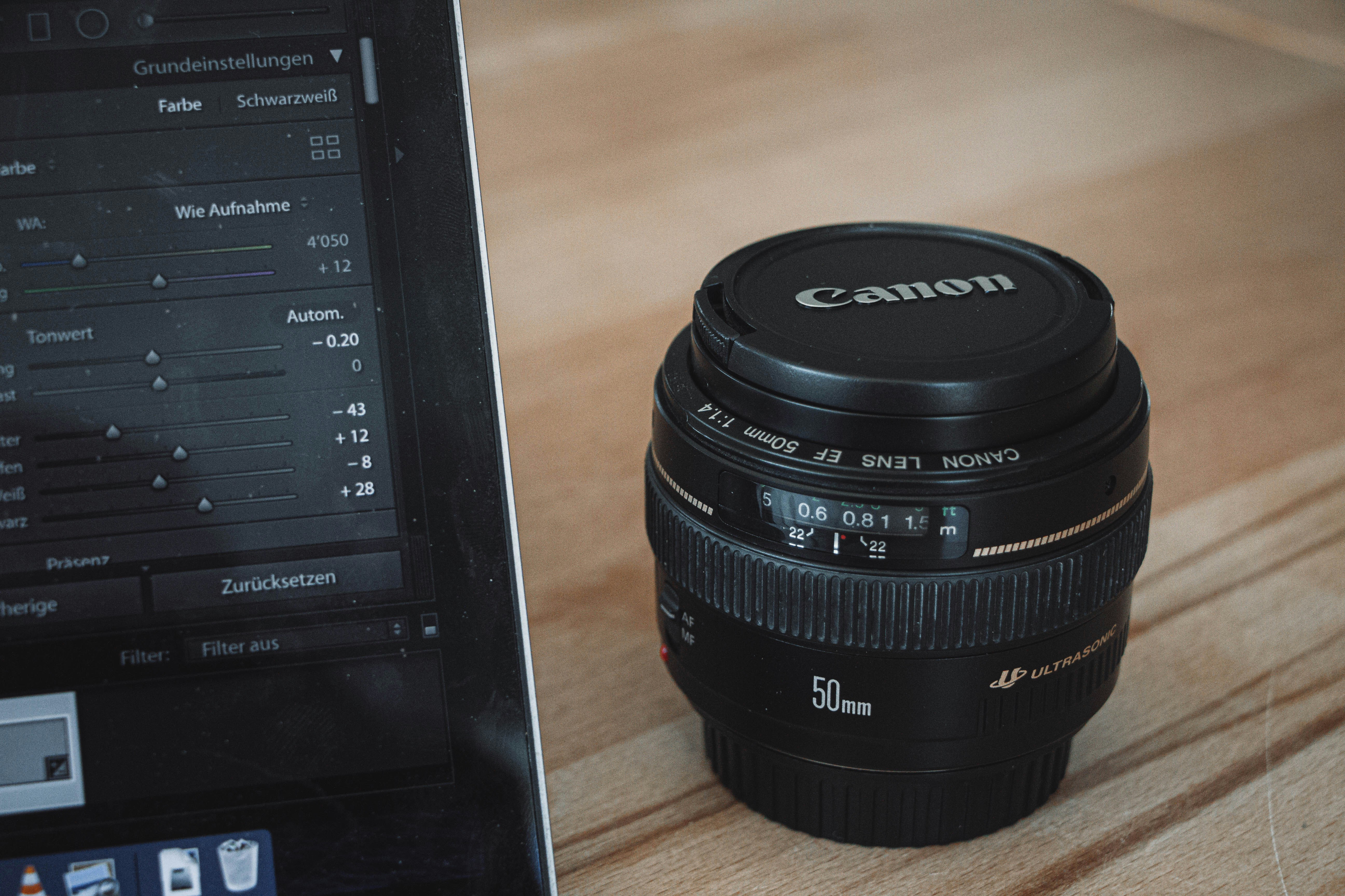 Desk-Side Study: Canon 50mm Prime Beside a Laptop on a Wooden Desk