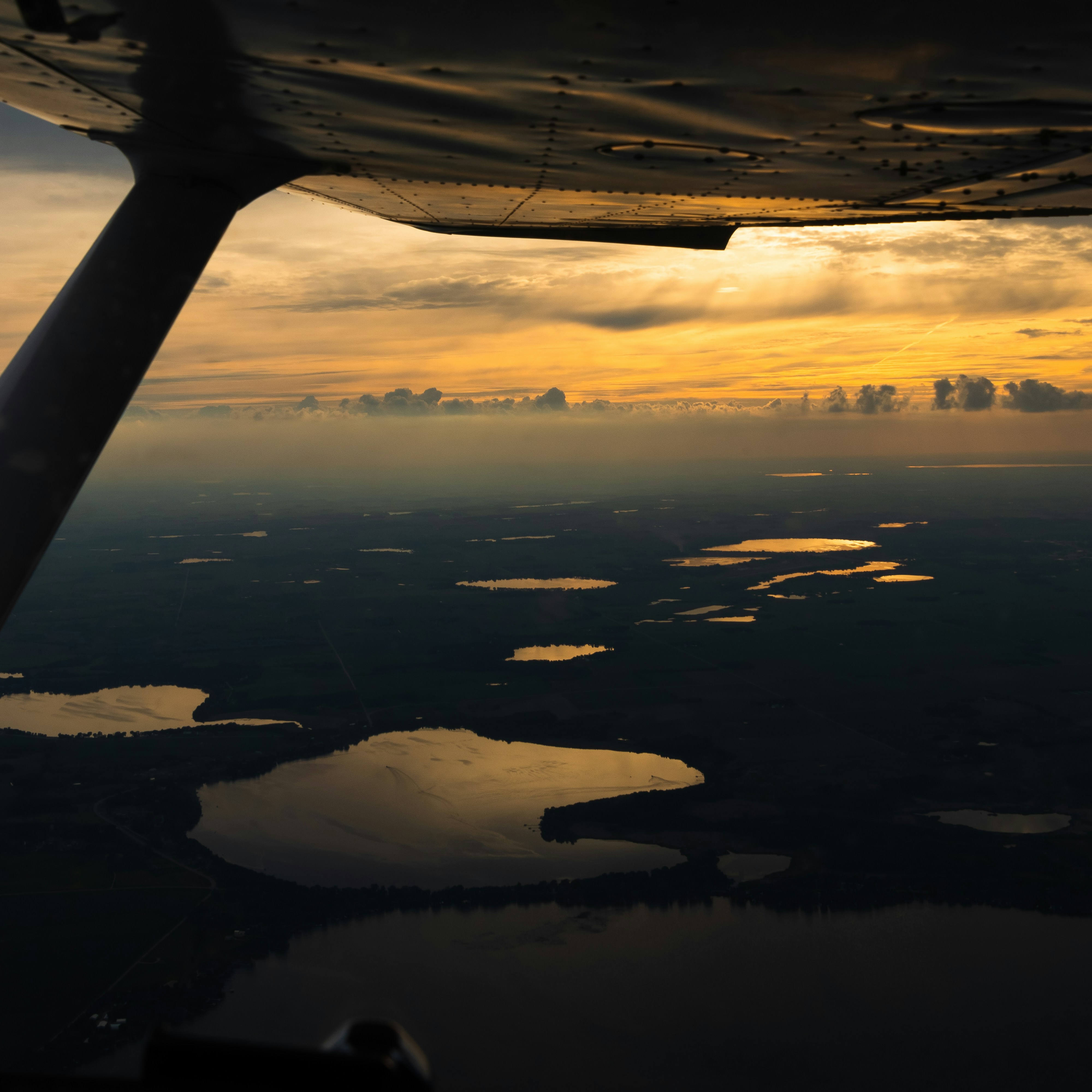 Aerial view showcasing shimmering lakes and a vibrant sunset sky, framed by the wing of an aircraft. The scene captures the serene beauty of nature from a unique perspective.