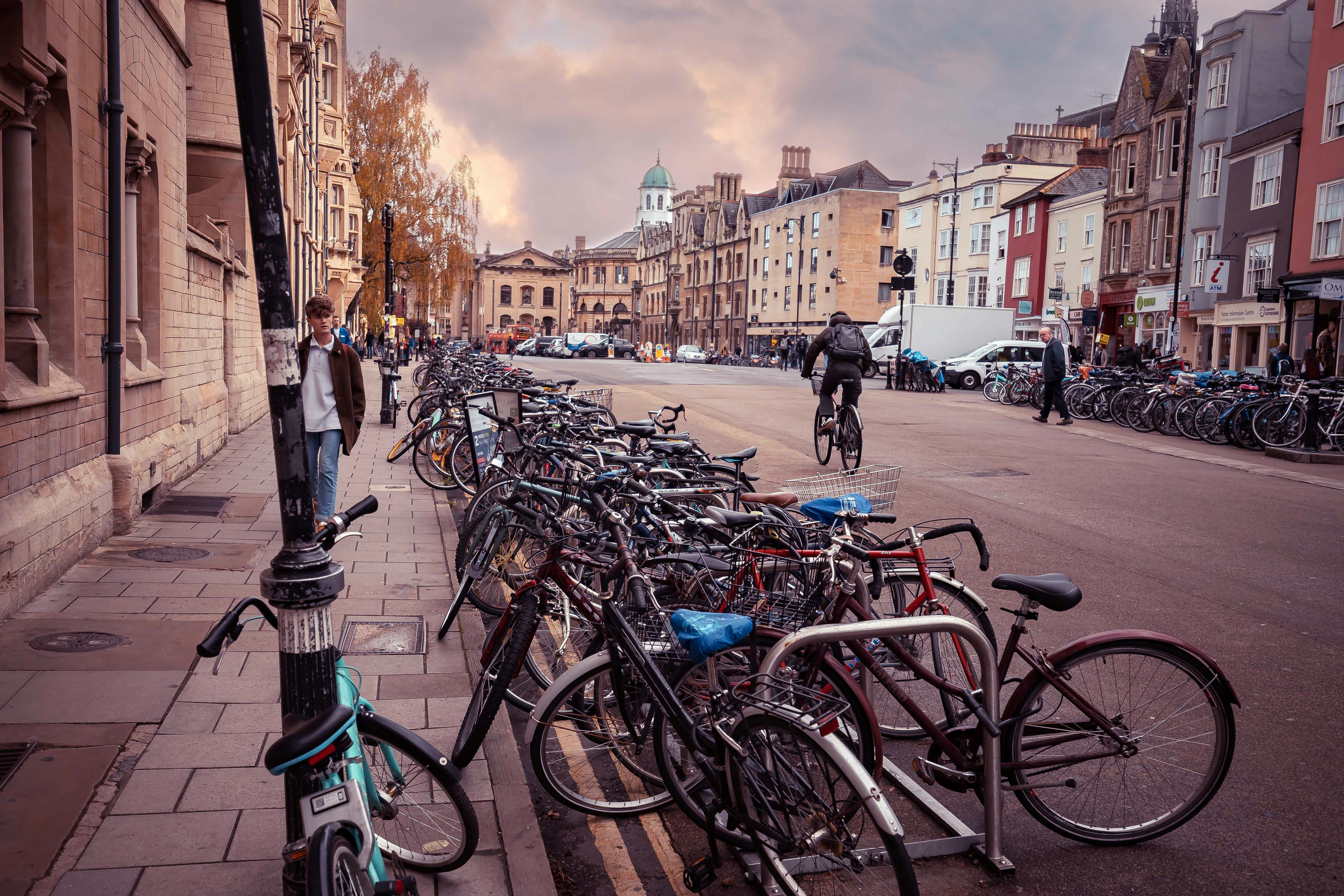 Bicycles lined up along a busy Oxford street under a dramatic sunset sky.