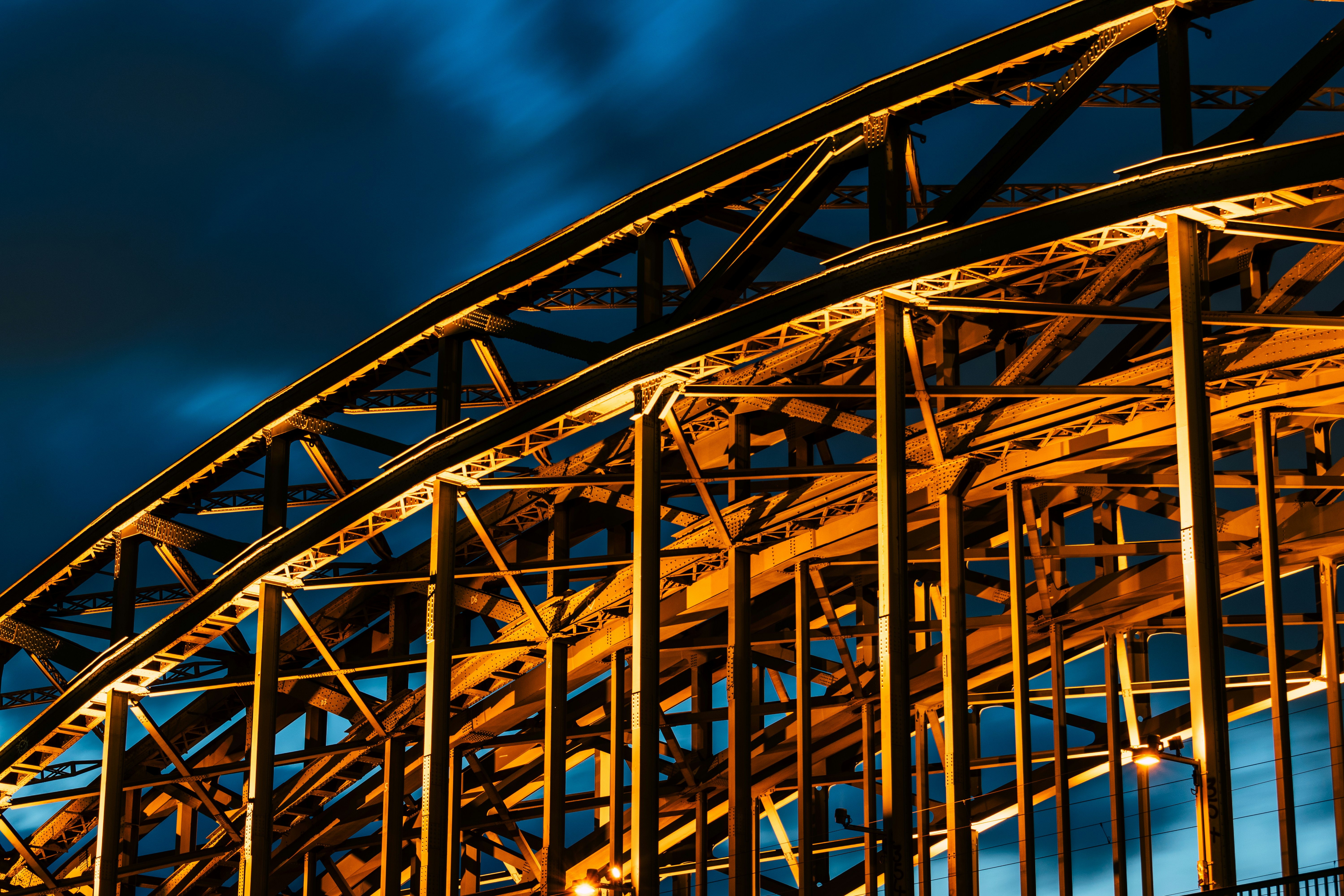 Illuminated bridge structure with intricate metalwork set against a deep blue evening sky.