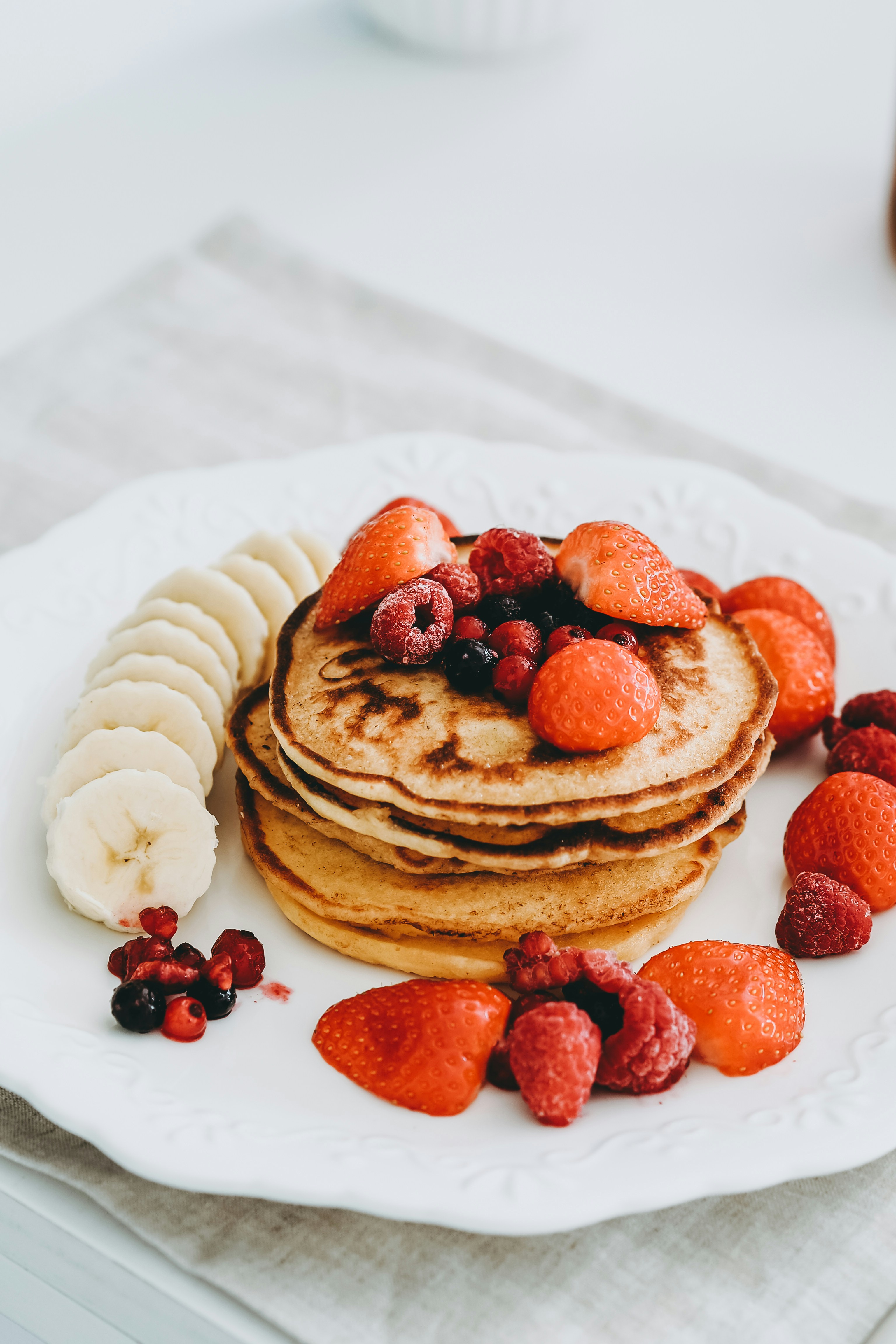 Stack of pancakes garnished with fresh strawberries, raspberries, and banana slices on a white plate.