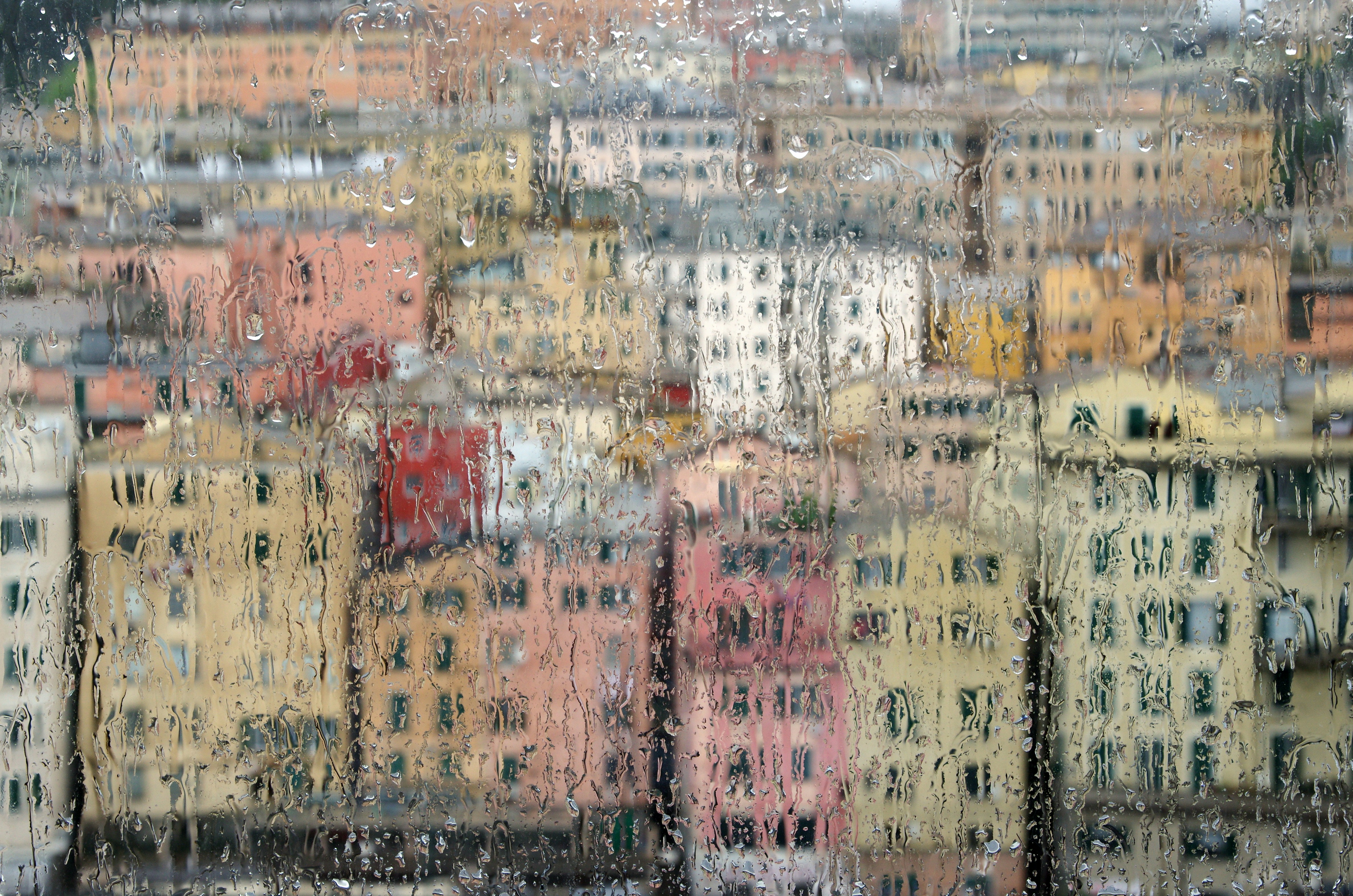 Colorful Genoa buildings blurred through rain-covered glass.