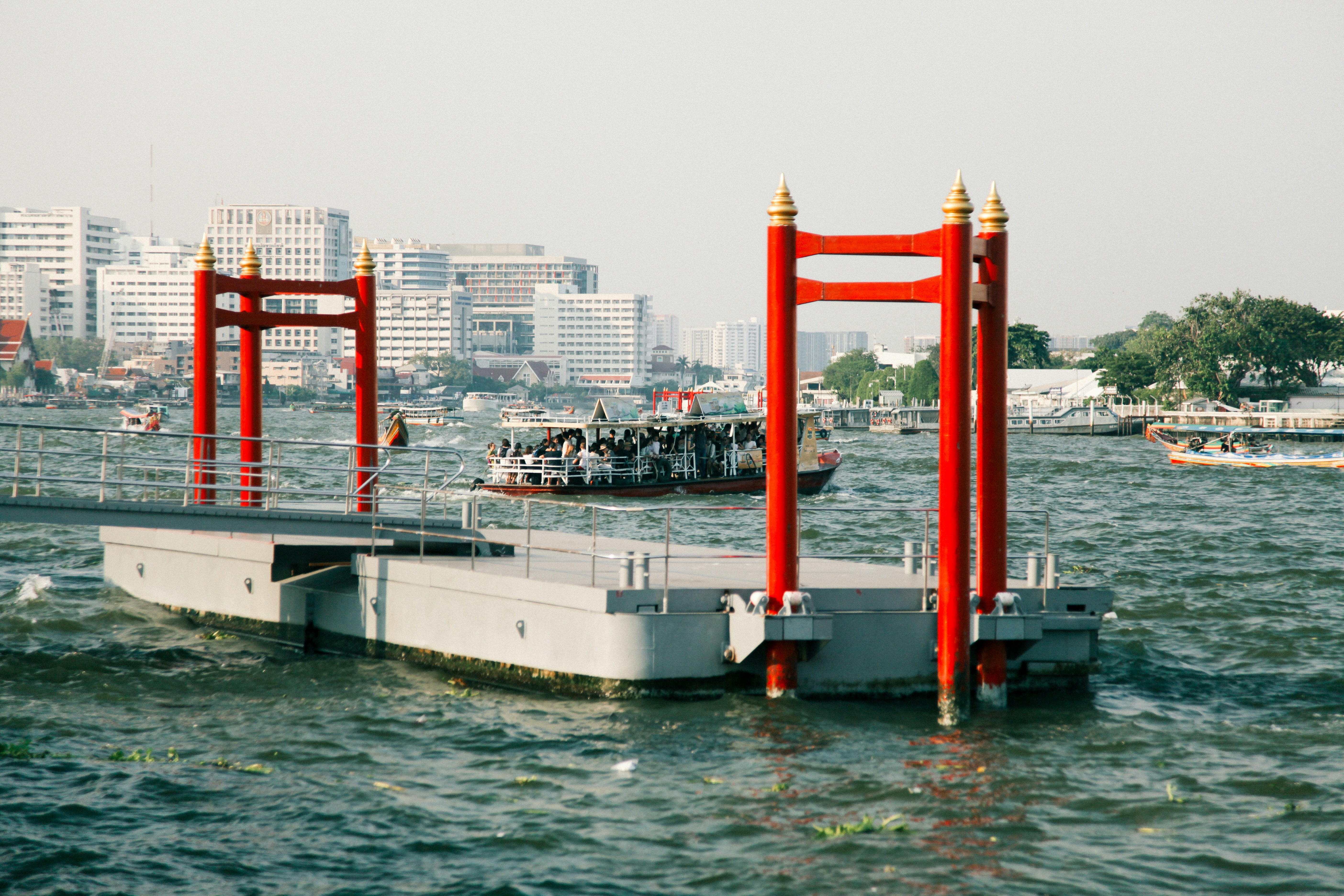 Scarlet Pylons Framing a Floating Dock Against an Urban Waterfront