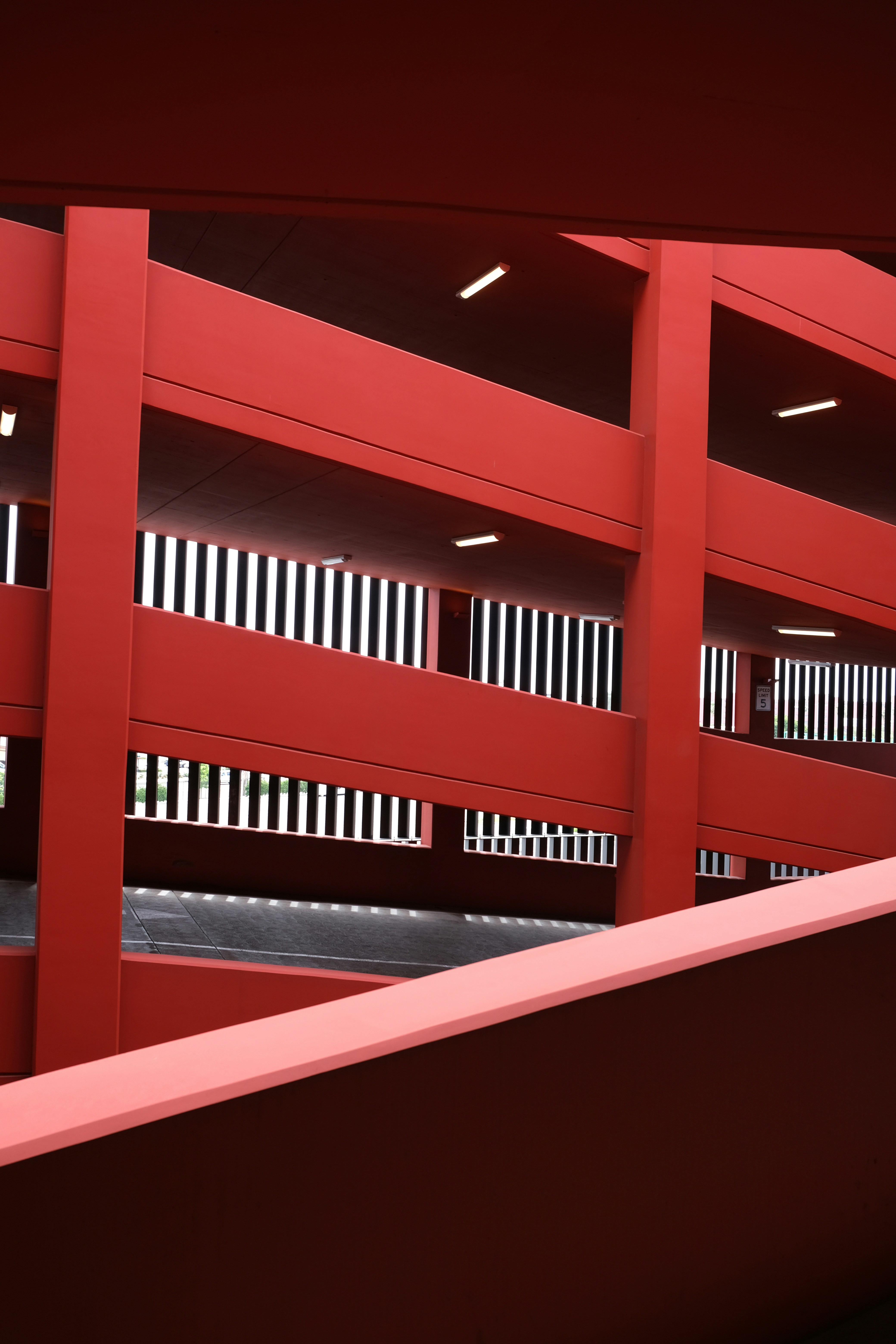Vibrant red structural beams intersect with contrasting vertical lines in a contemporary parking facility, highlighting modern design elements.