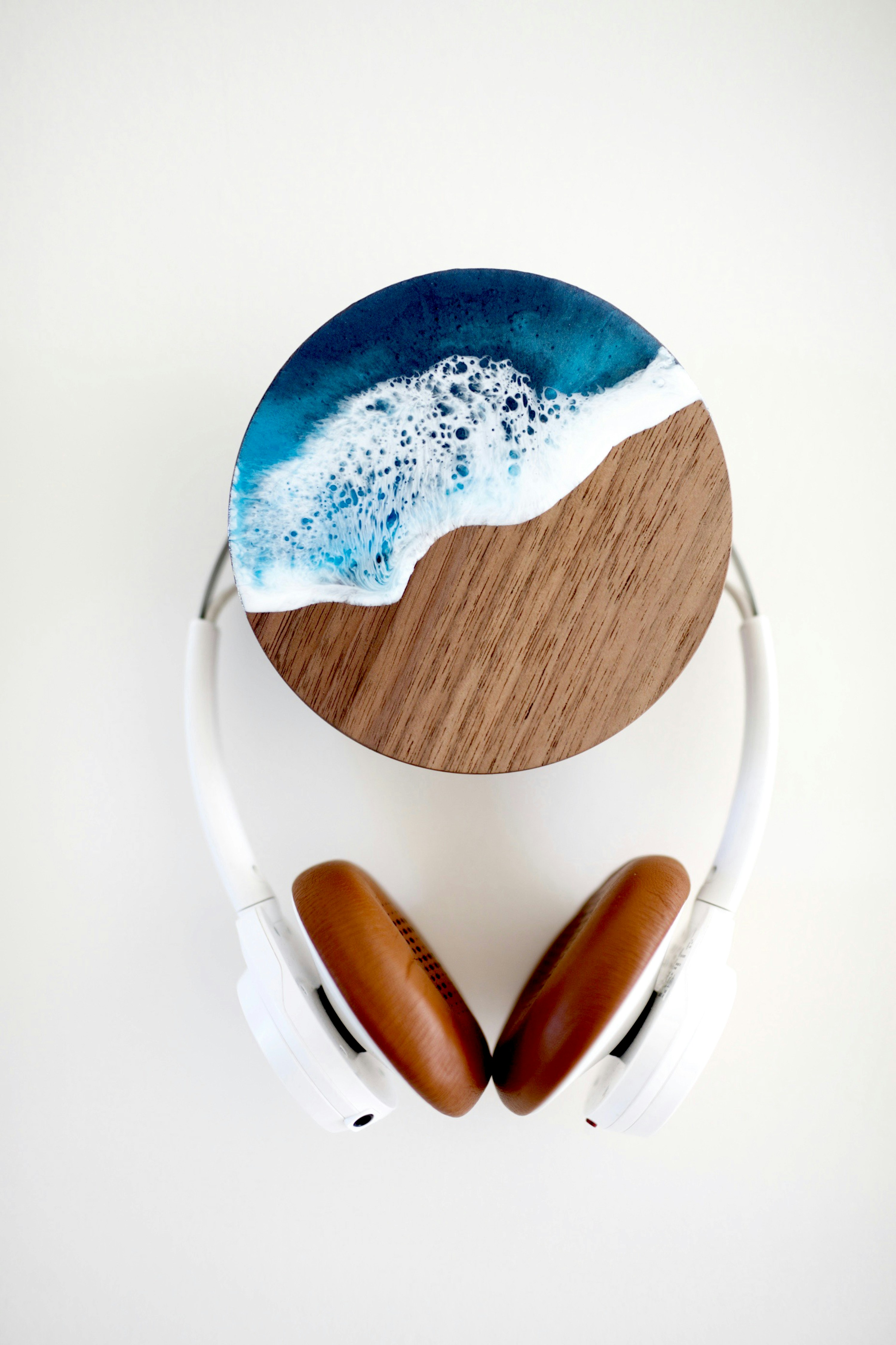 Stylized wooden coaster featuring a wave design atop a pair of white headphones. The composition blends natural elements with modern audio equipment.