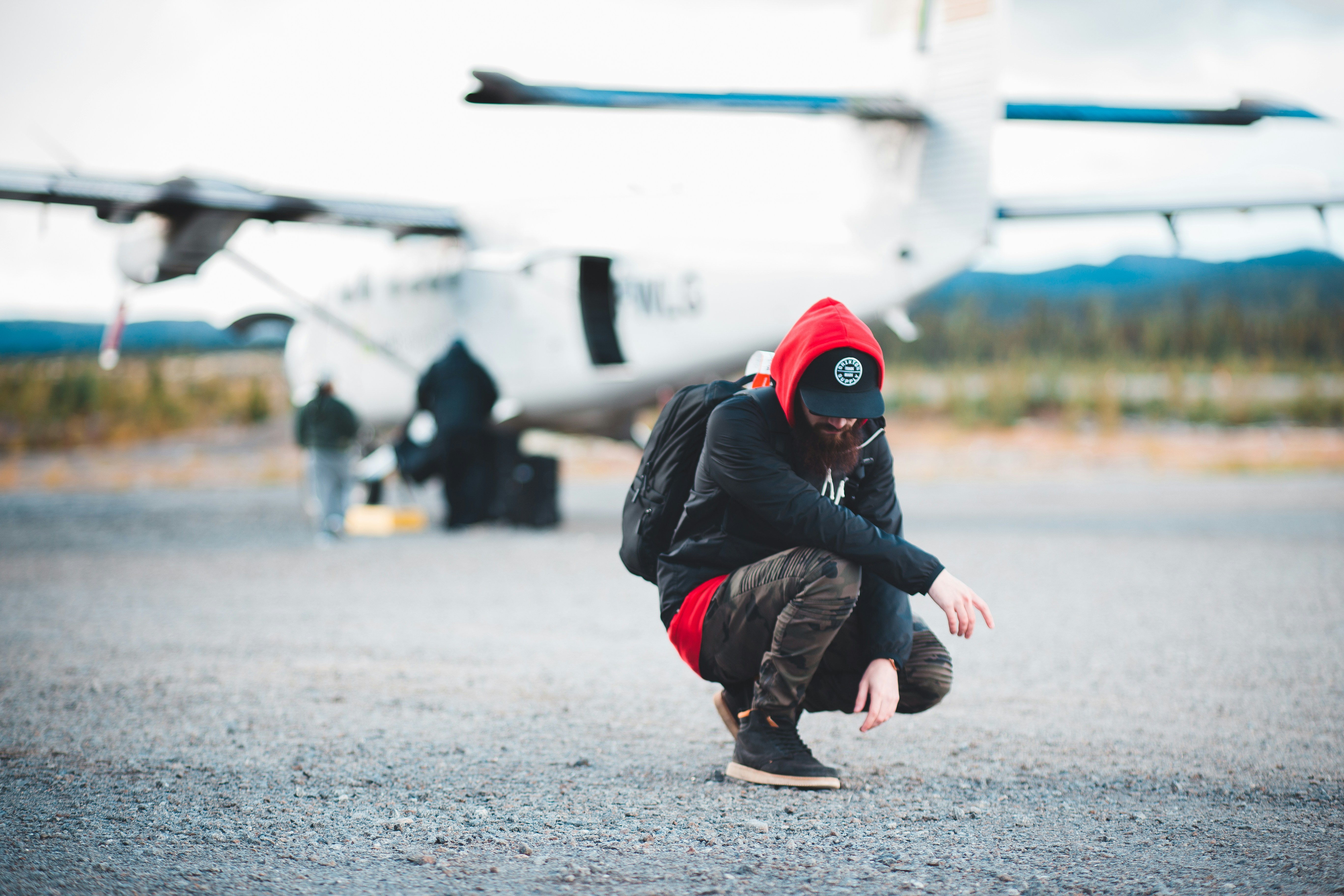Red-Hooded Figure on an Empty Airfield beside a Dormant Propeller Plane