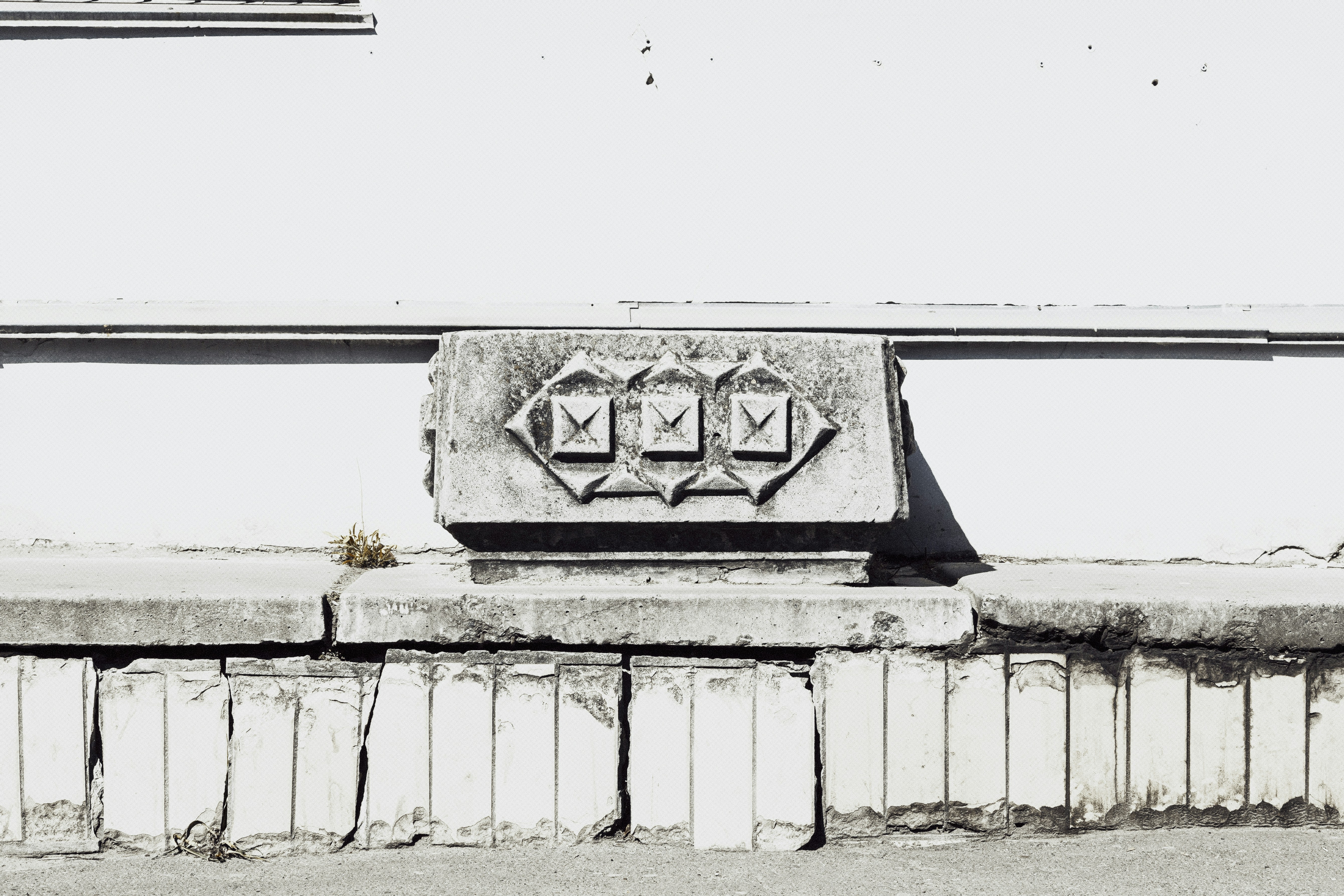 Ornate stone pedestal with geometric carvings against a stark white wall, showcasing the passage of time and neglect.
