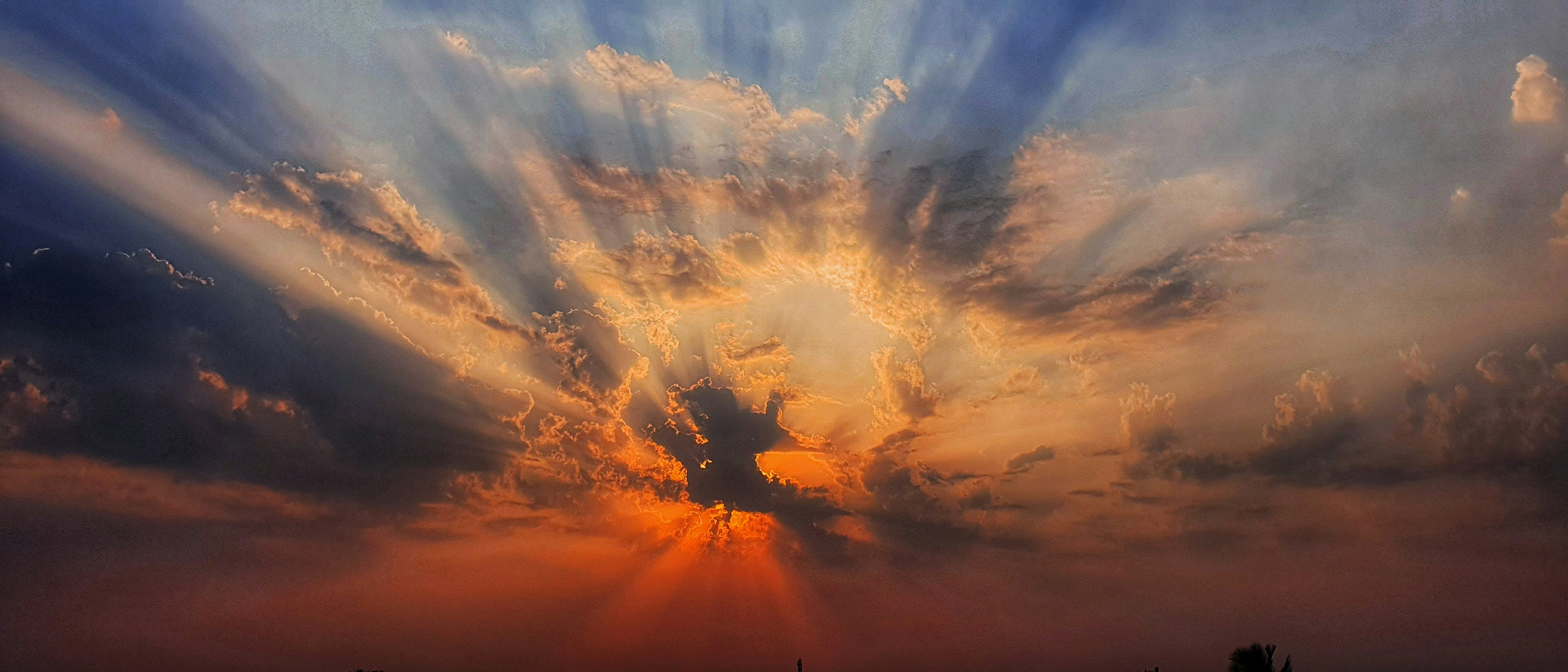 Radiant sunbeams pierce through a tapestry of clouds during sunset, creating a dramatic interplay of light and color.