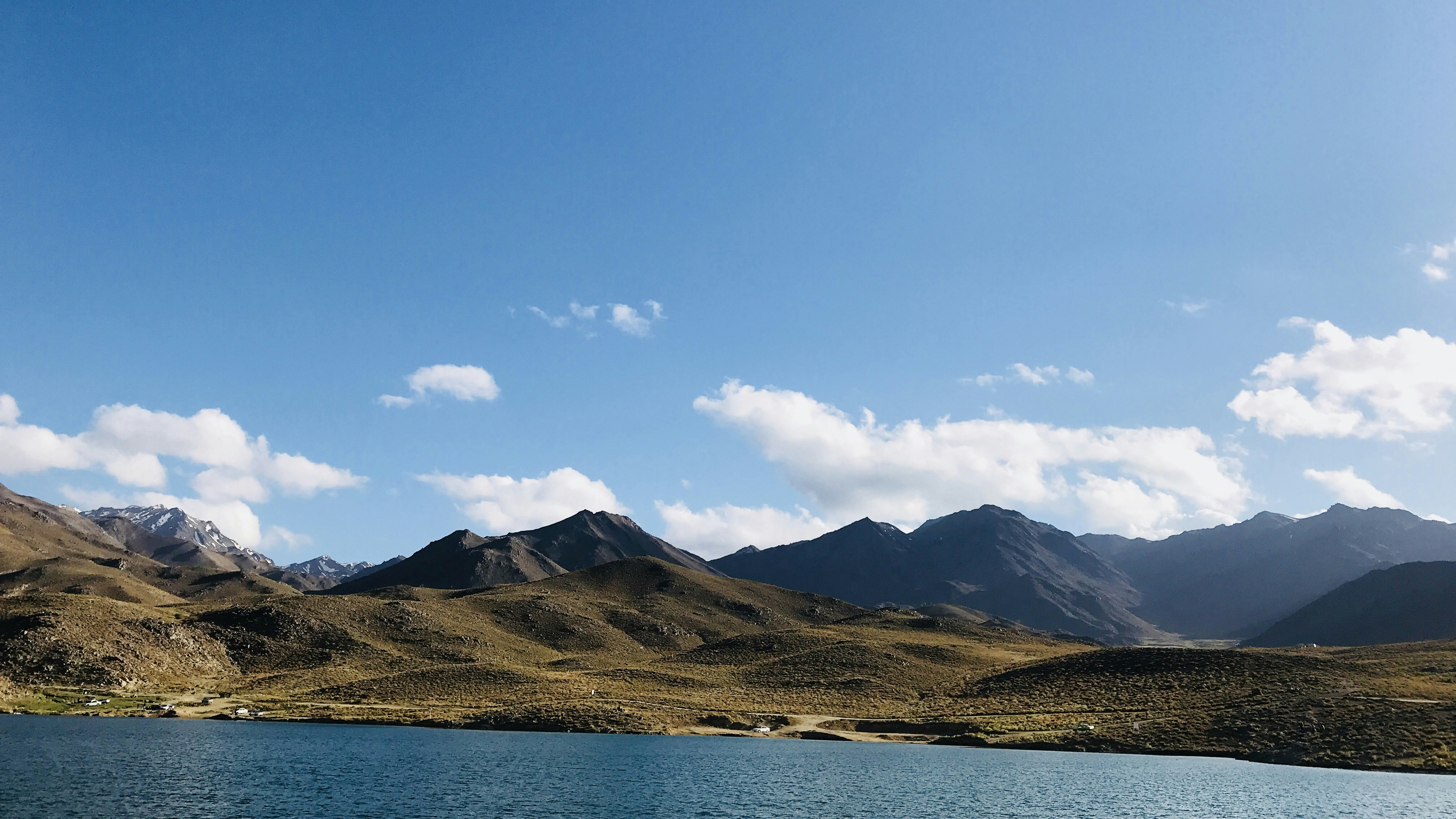 Serene landscape showcasing rolling hills and majestic mountains under a clear blue sky, reflecting in the tranquil lake below.