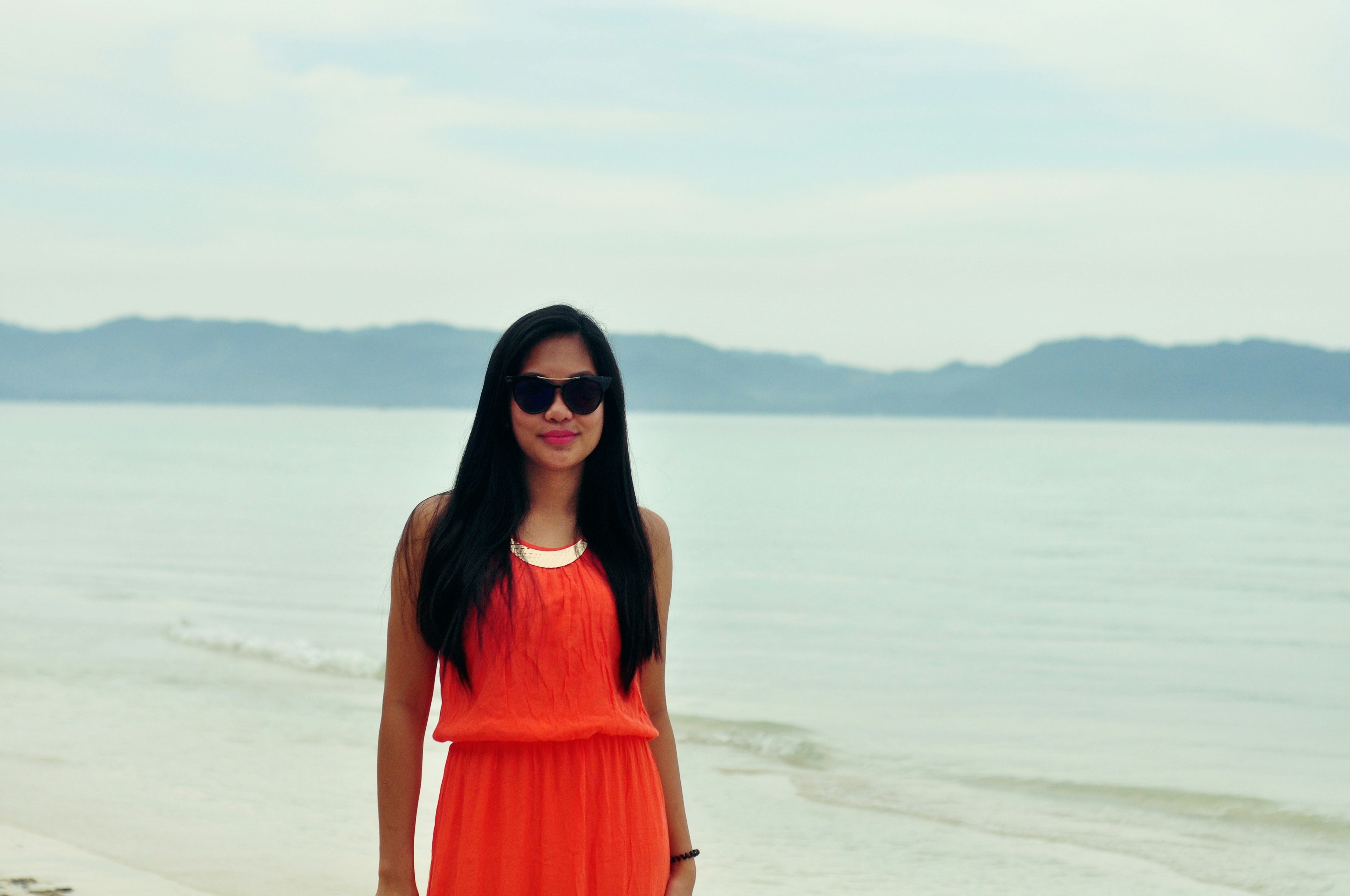 Orange dress on the shoreline: a portrait against distant mountains