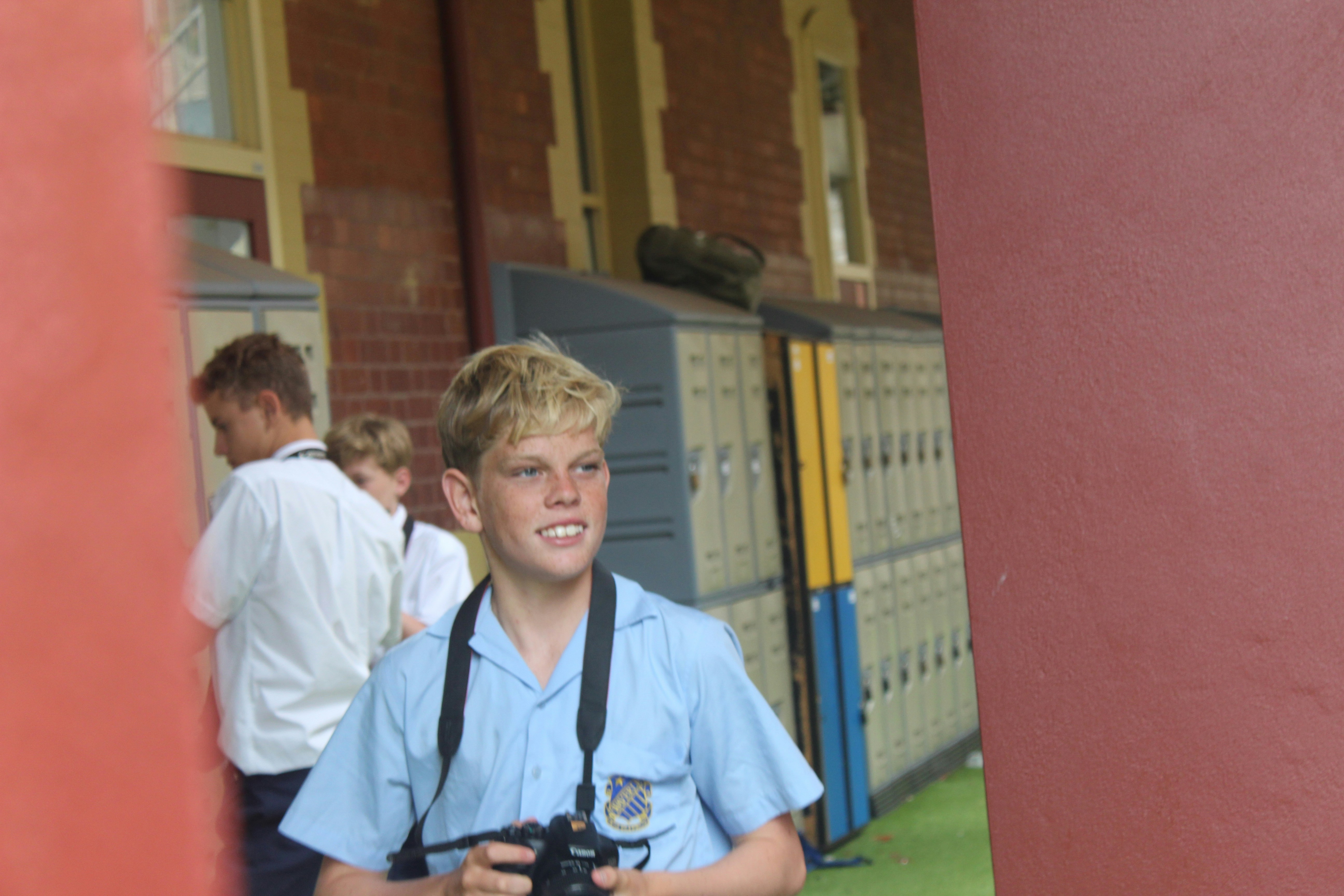 Young photographer holding a camera, surrounded by school lockers and peers, capturing a moment of inspiration.