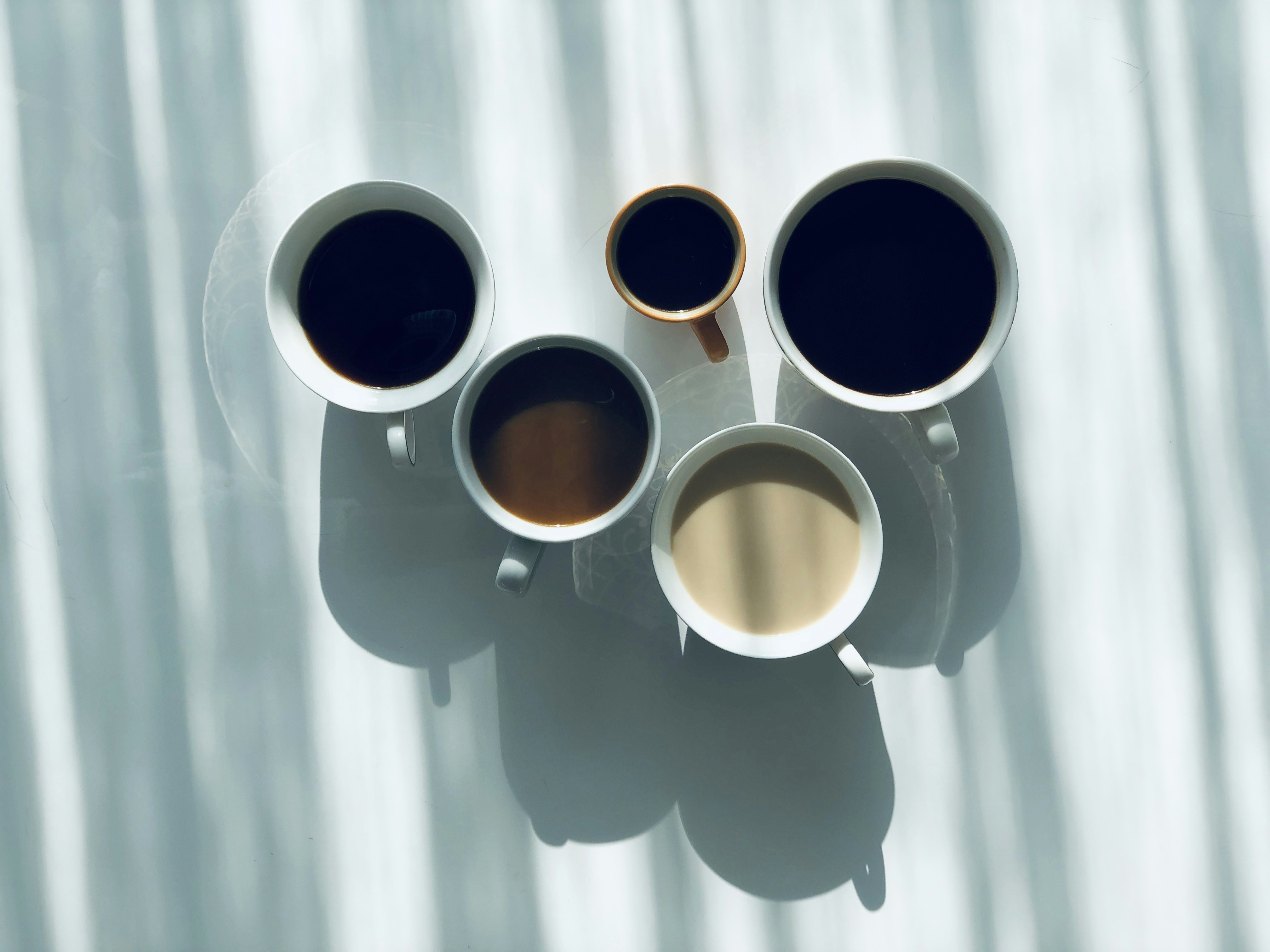 Assorted coffee cups casting long shadows on a sunlit surface.