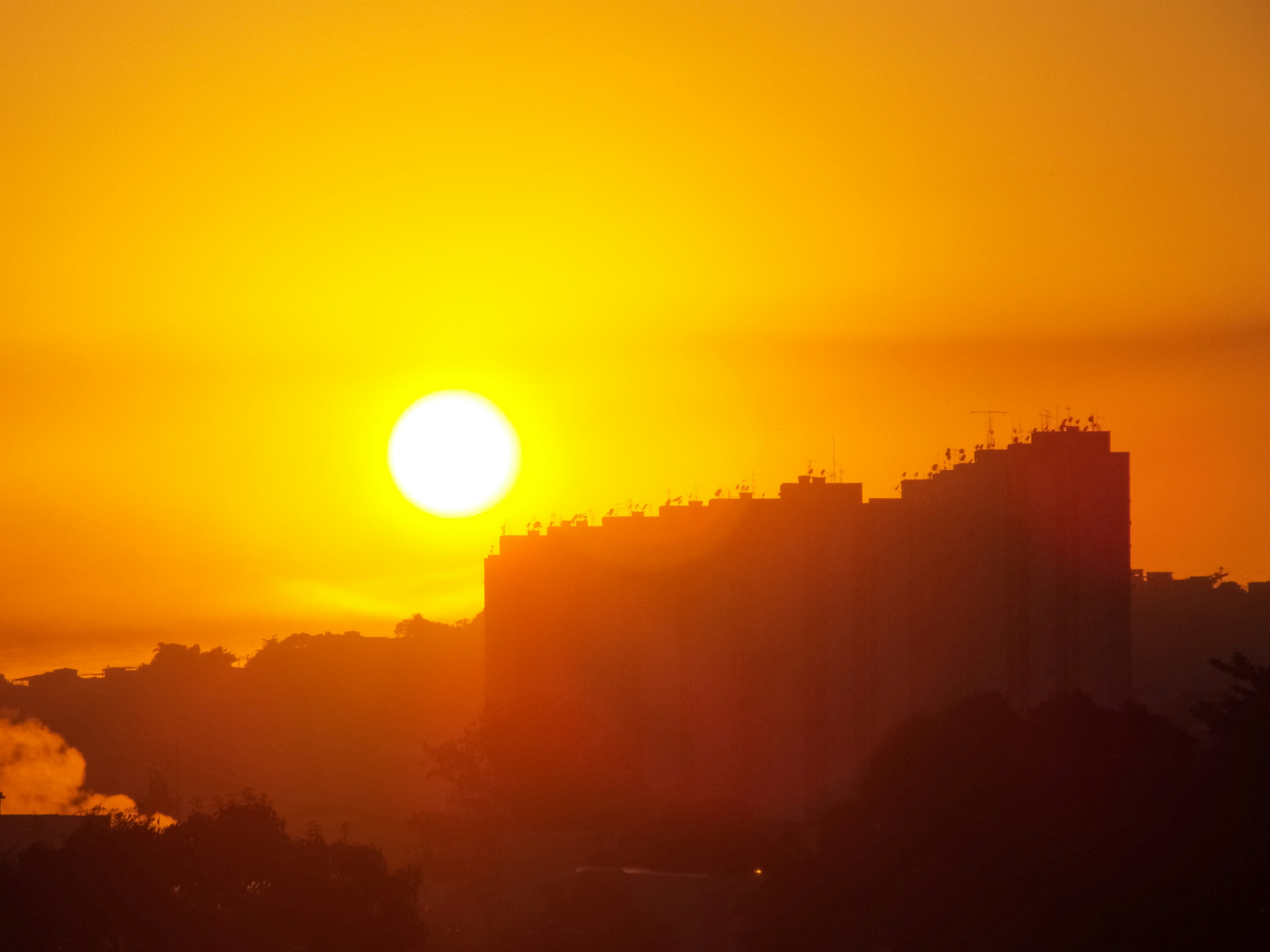 Silhouetted buildings and trees framed by a vibrant orange sunset.