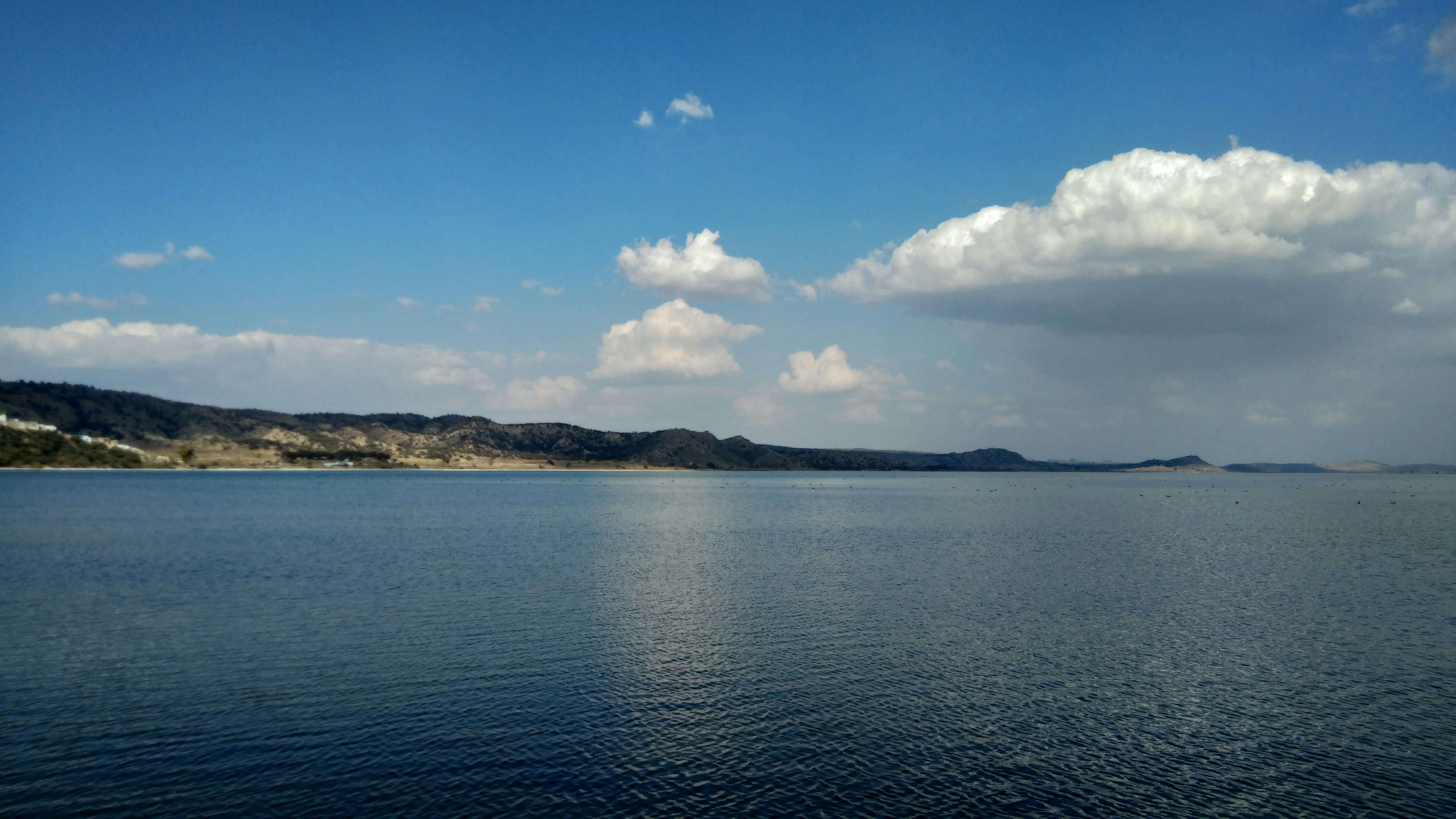 Wide expanse of calm lake under a bright blue sky with scattered clouds.