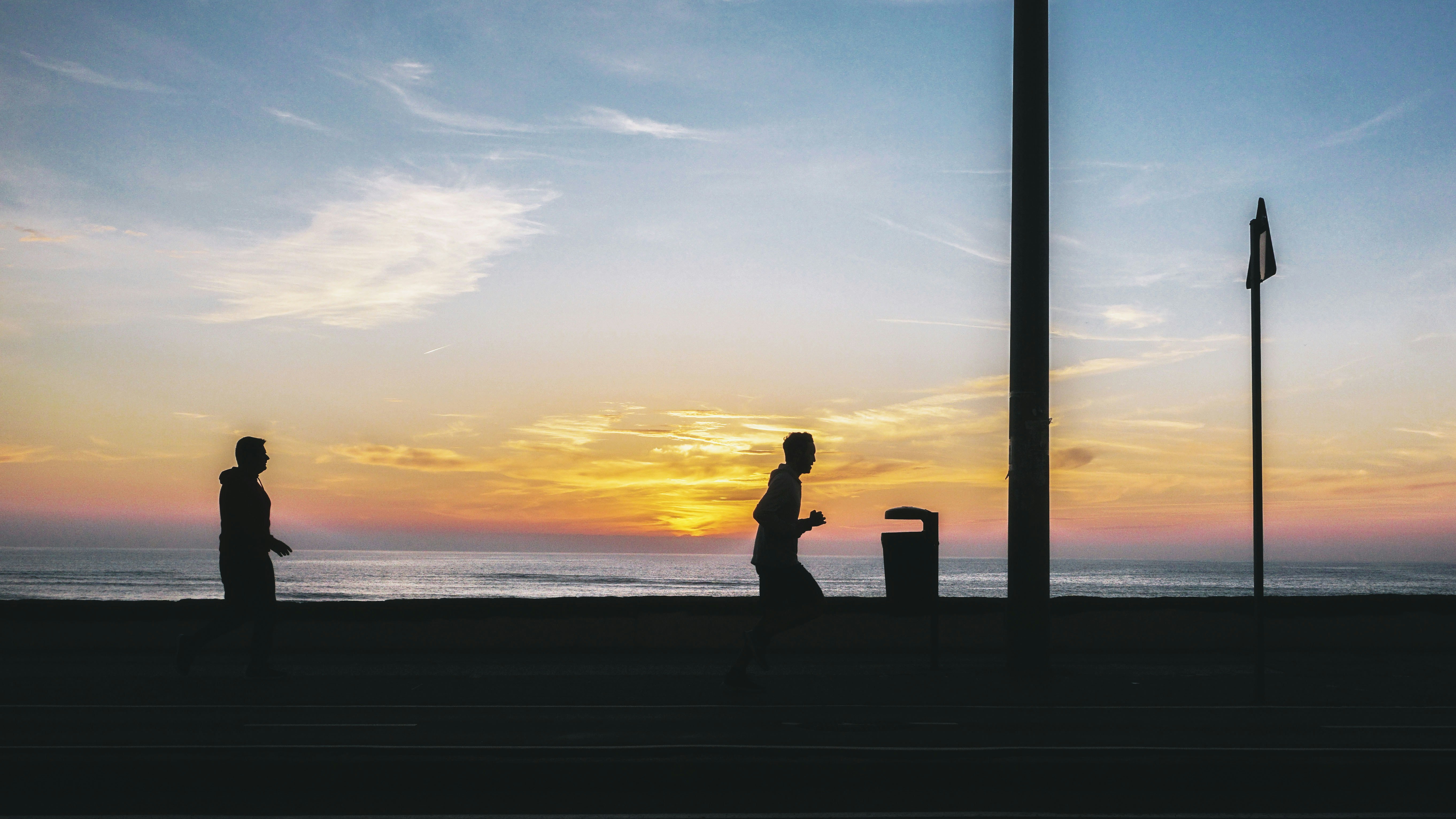 Silhouettes of two joggers on a boardwalk against a vibrant sunset over the ocean.