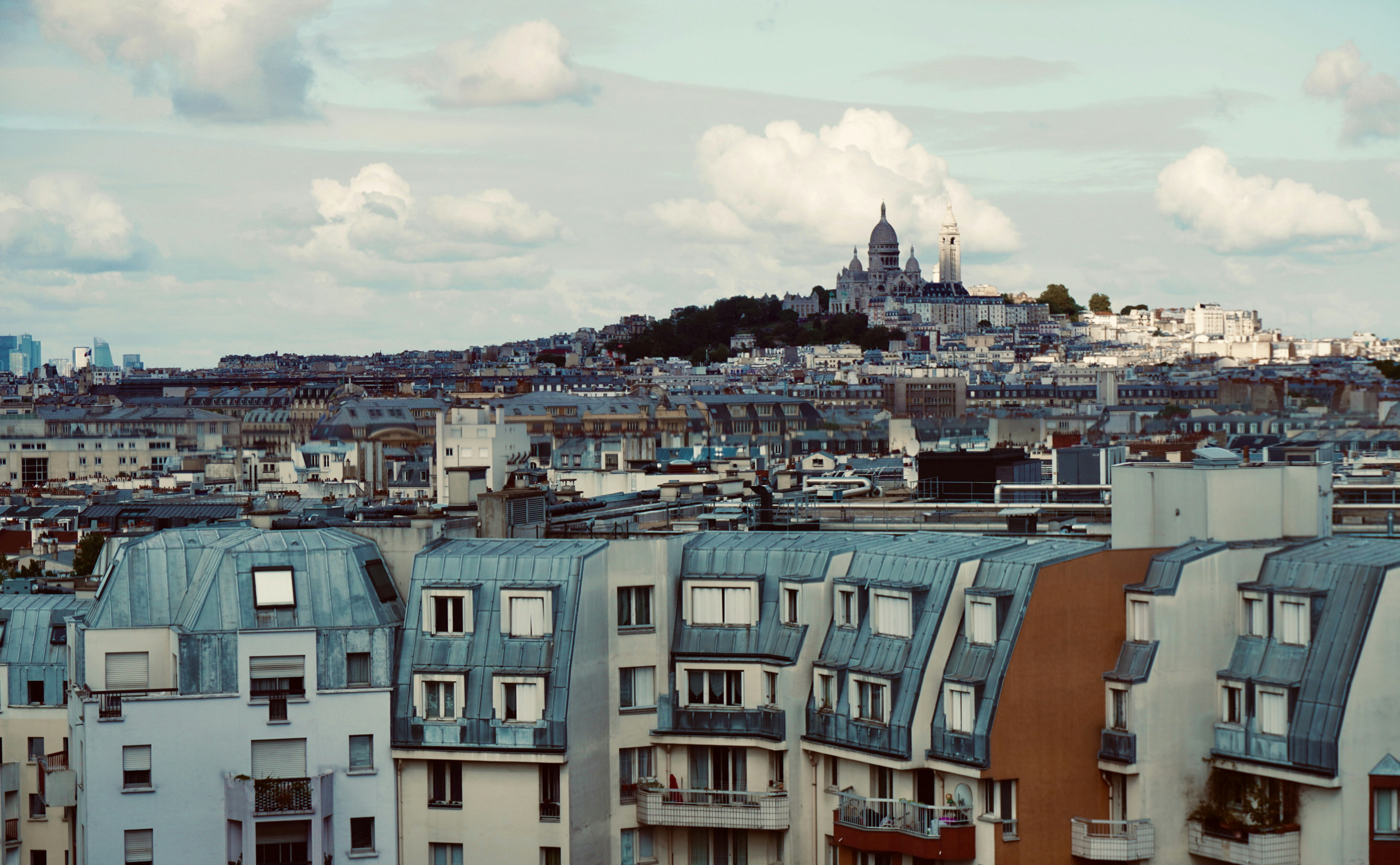 View of Paris rooftops with Montmartre in the background, showcasing the city's architectural diversity under a cloudy sky.
