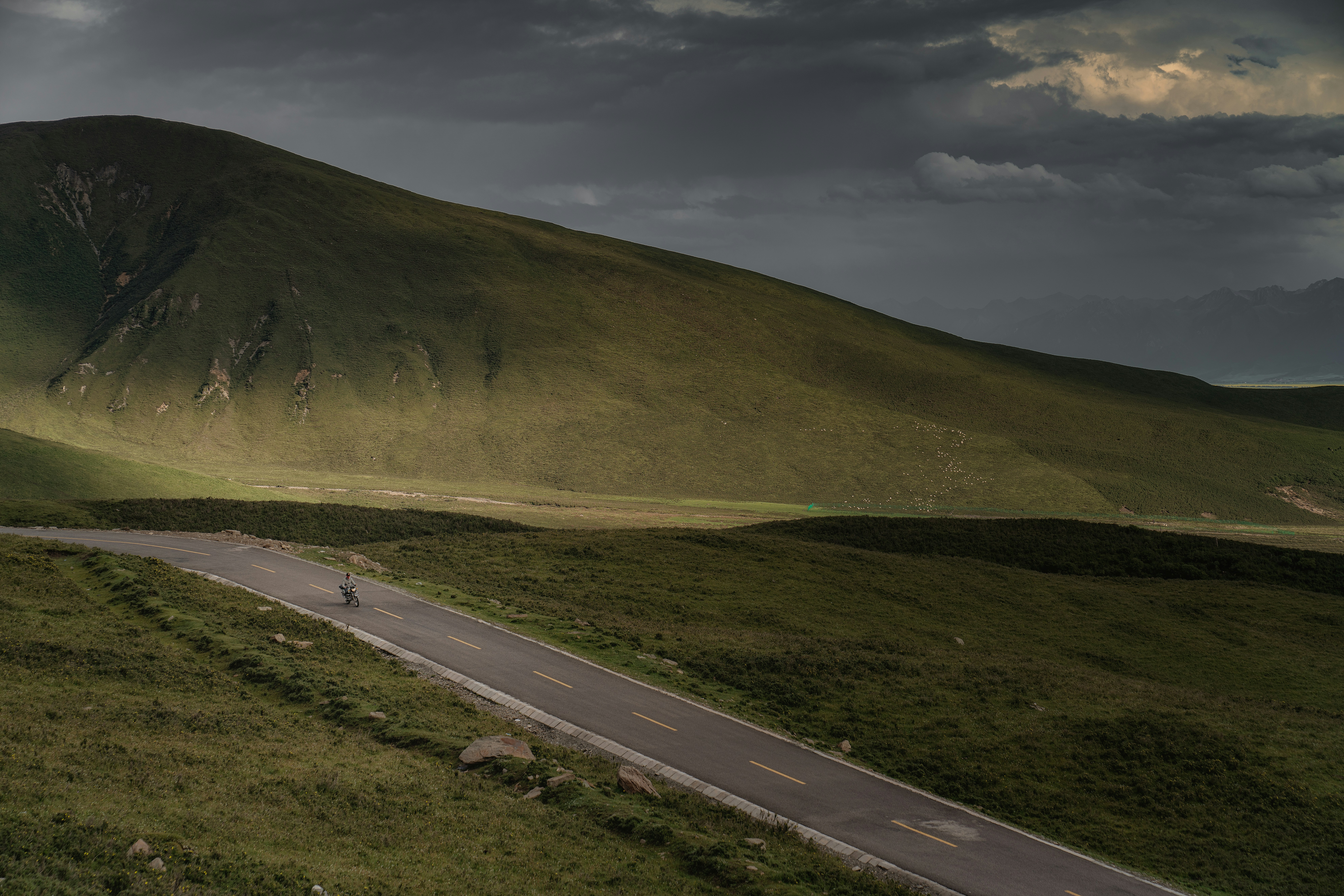 A Lonely Rider | gray asphalt road between green grass field under cloudy sky during daytime